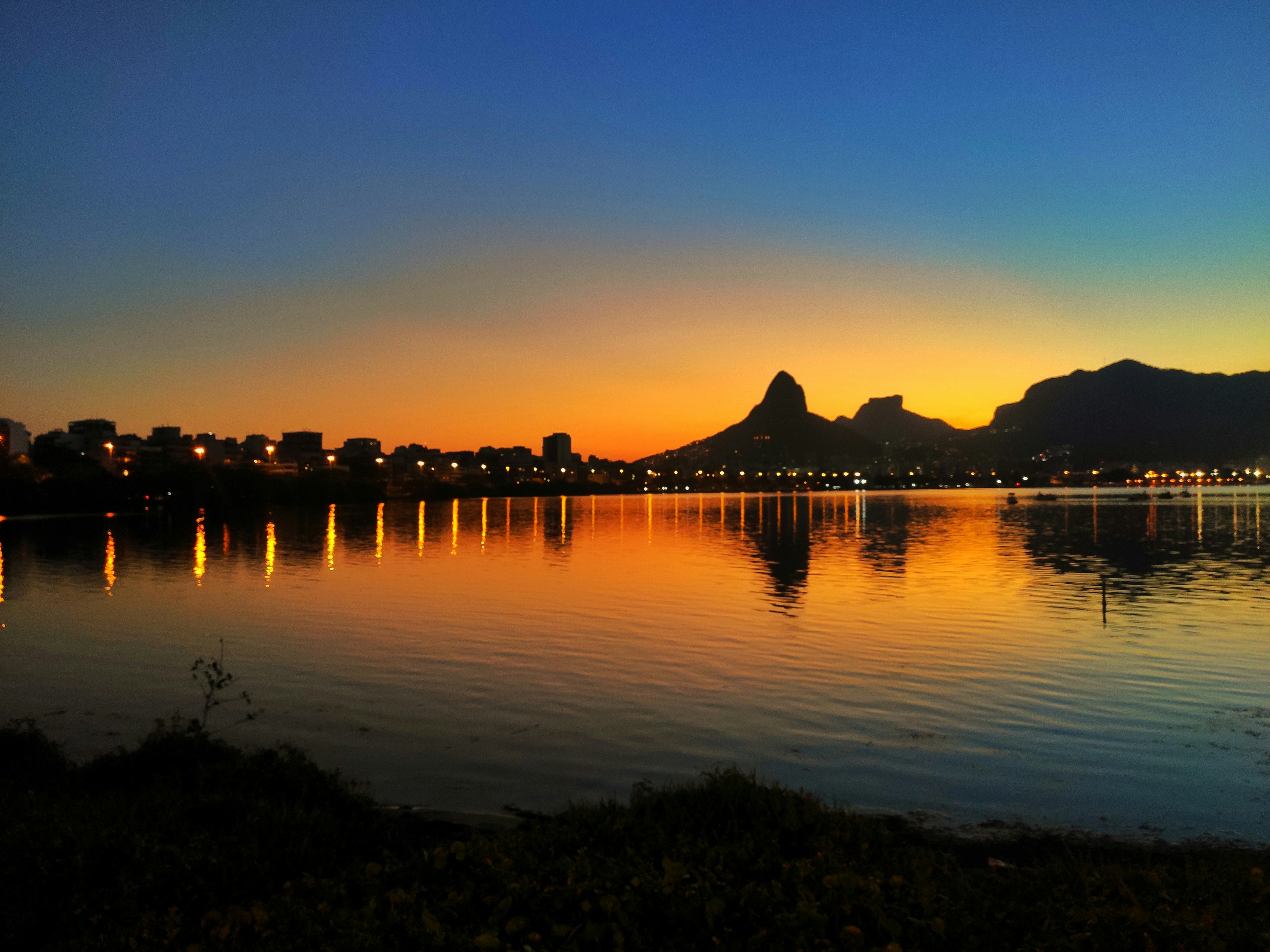 City skyline silhouetted against a vibrant sunset with reflections on calm water.