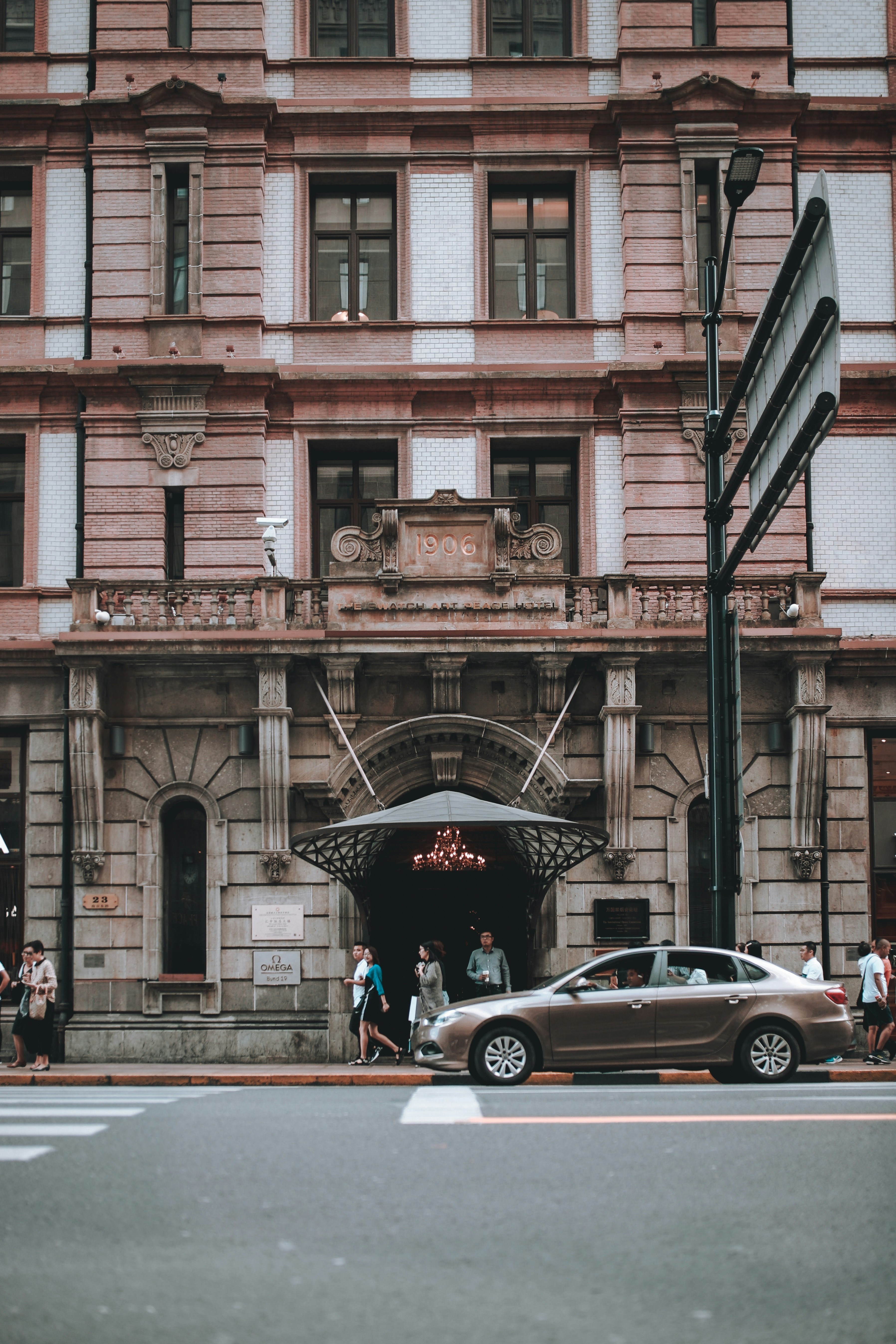 Archway of Time: Pedestrians and a Sedan Before a 1906 Facade