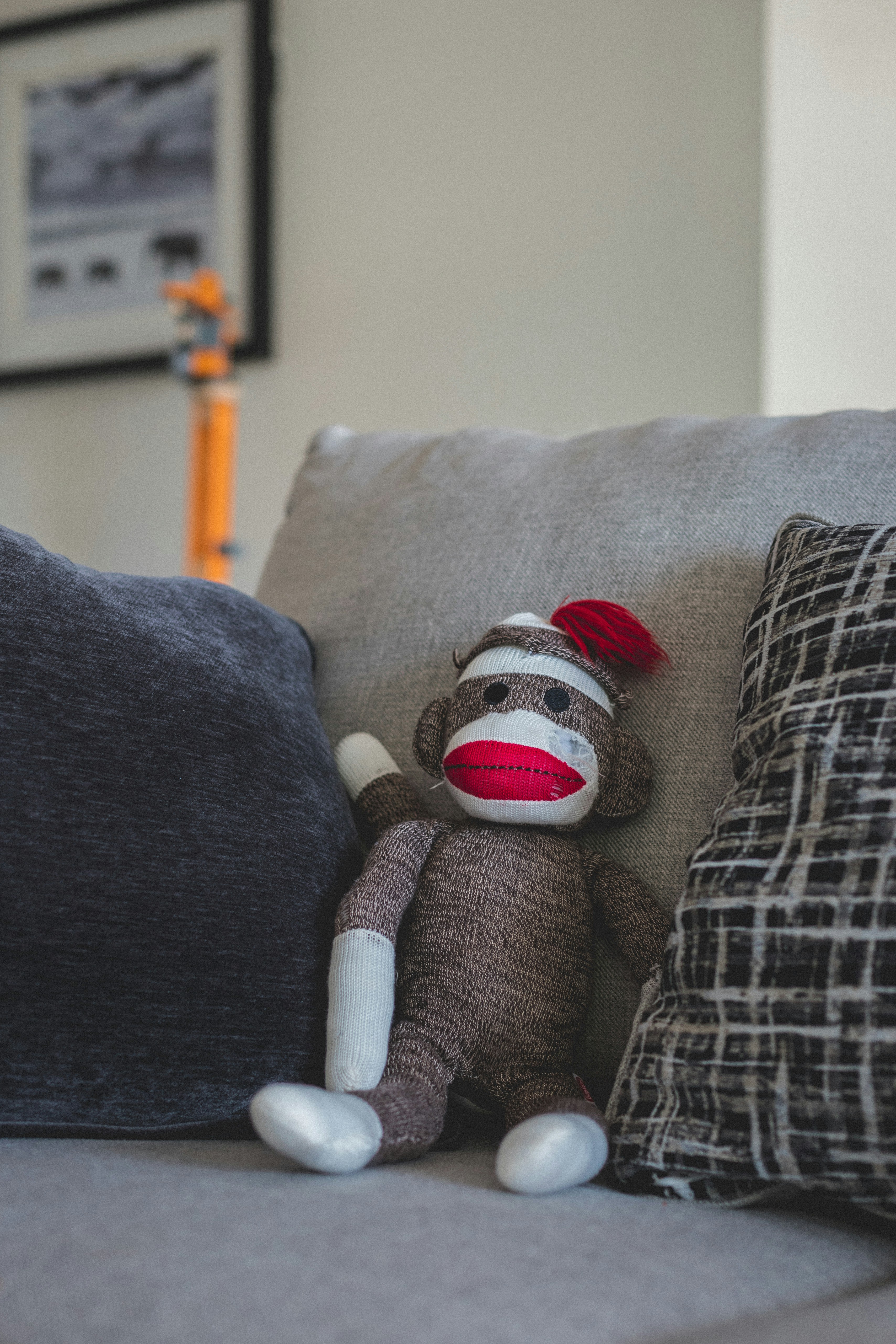 Sock Monkey on a Cozy Couch framed by Pillows and a Glimpsed Toy Tripod