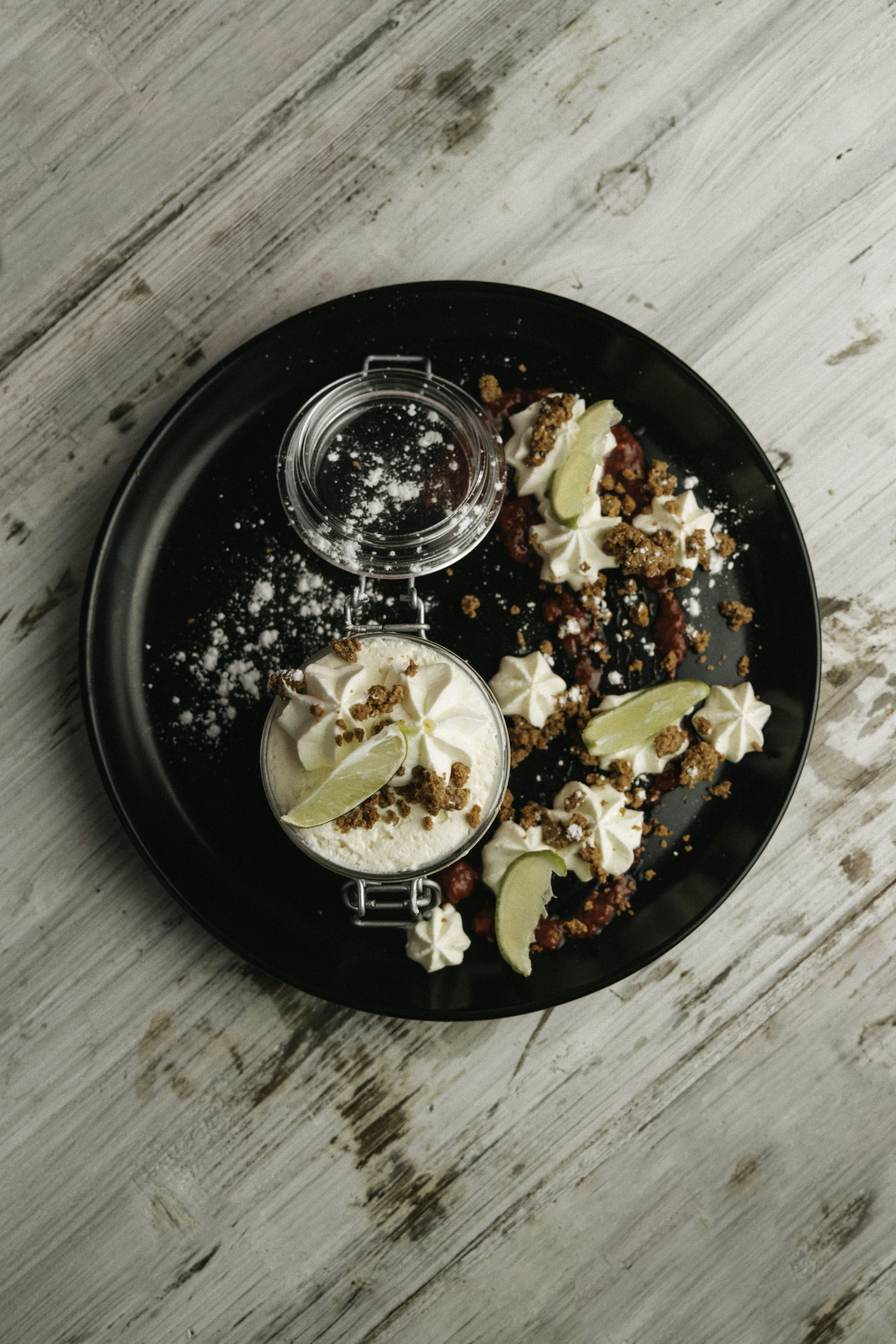 A black plate adorned with creamy desserts, garnished with lime slices and crushed toppings, set against a rustic wooden background.