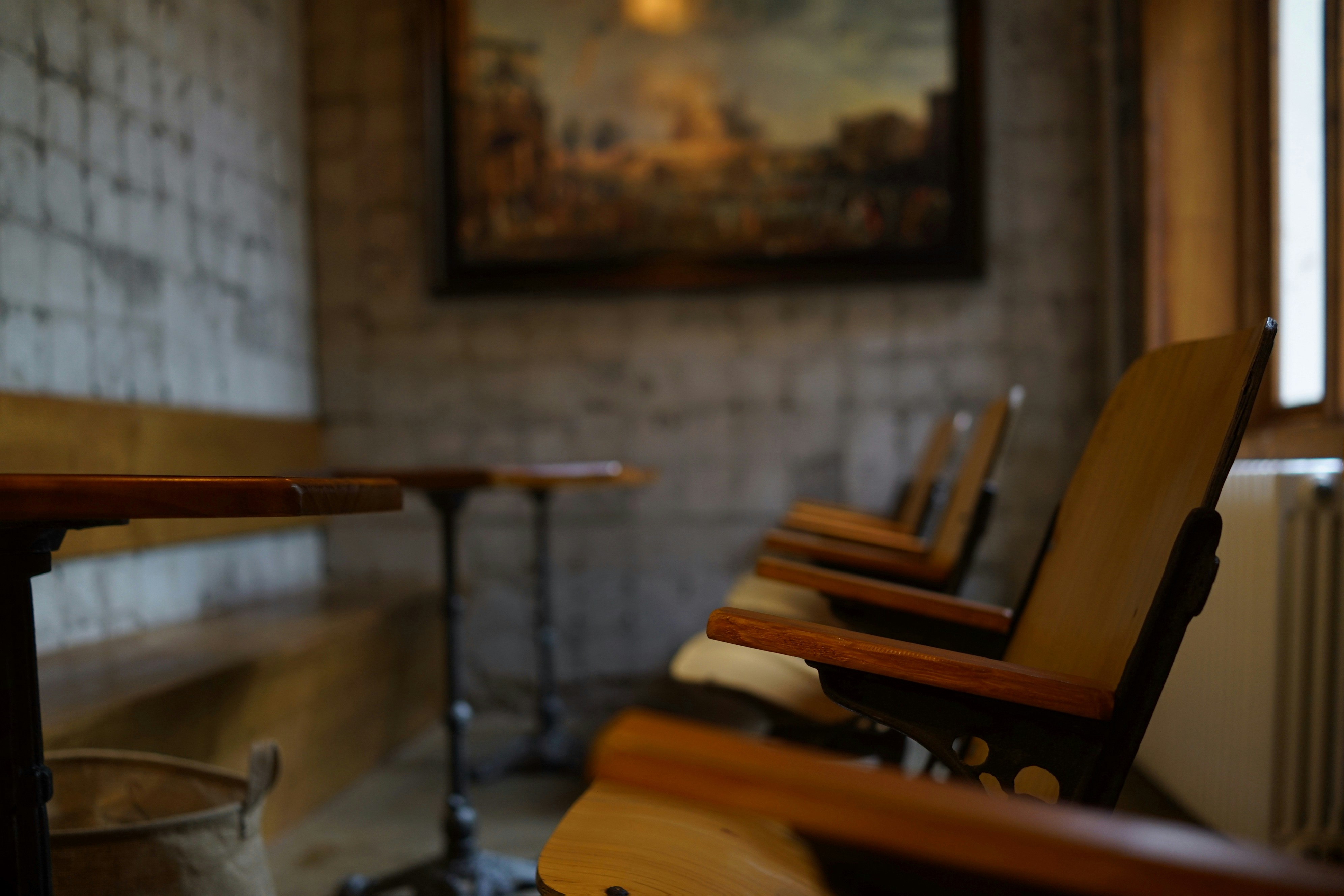 Wooden chairs arranged around rustic tables in a softly lit room, with a vintage painting adorning the wall. The ambiance suggests a serene gathering space.