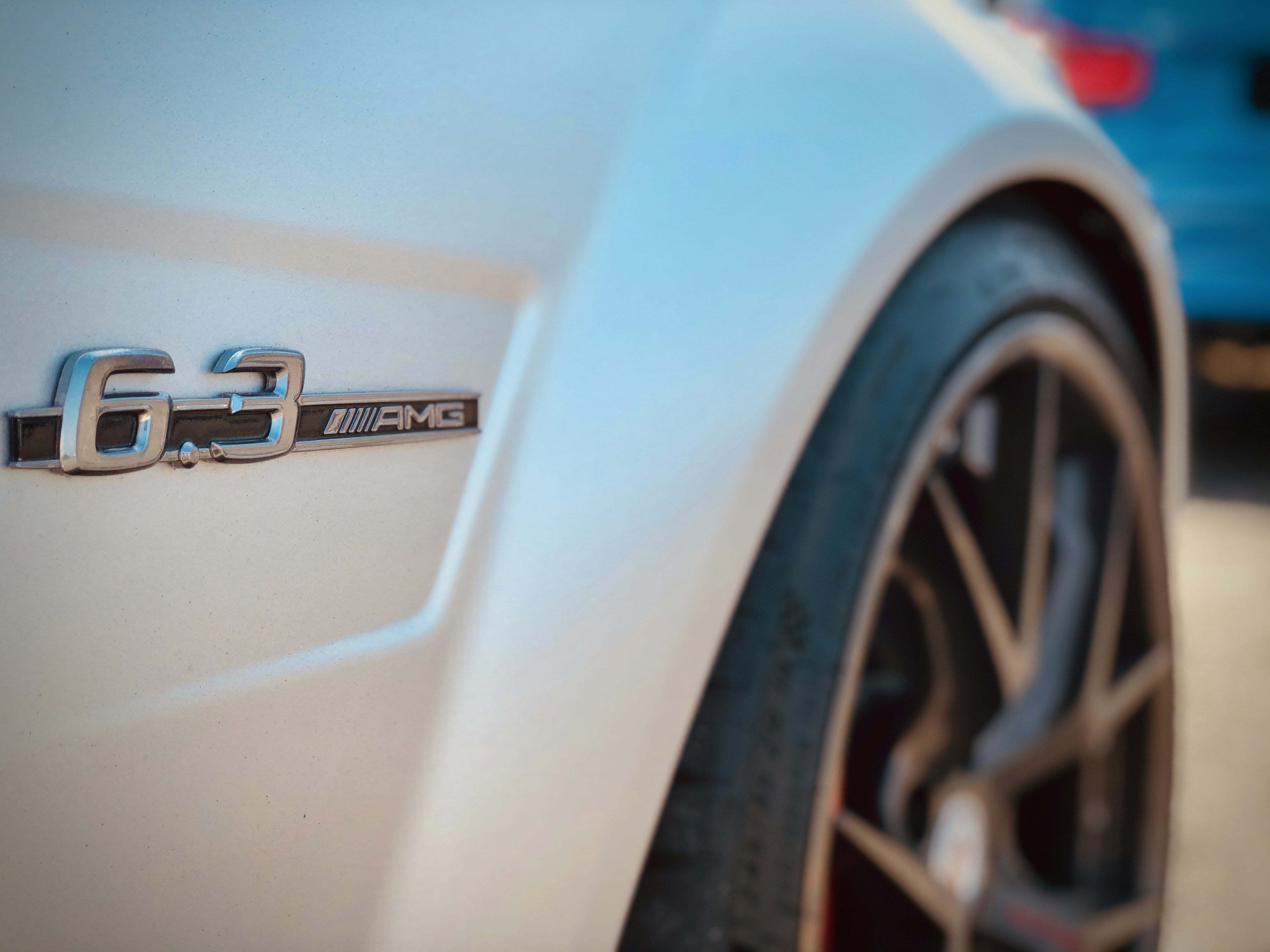 Close-up of a car's wheel and badge on a white fender, emphasizing sleek design and luxury branding.