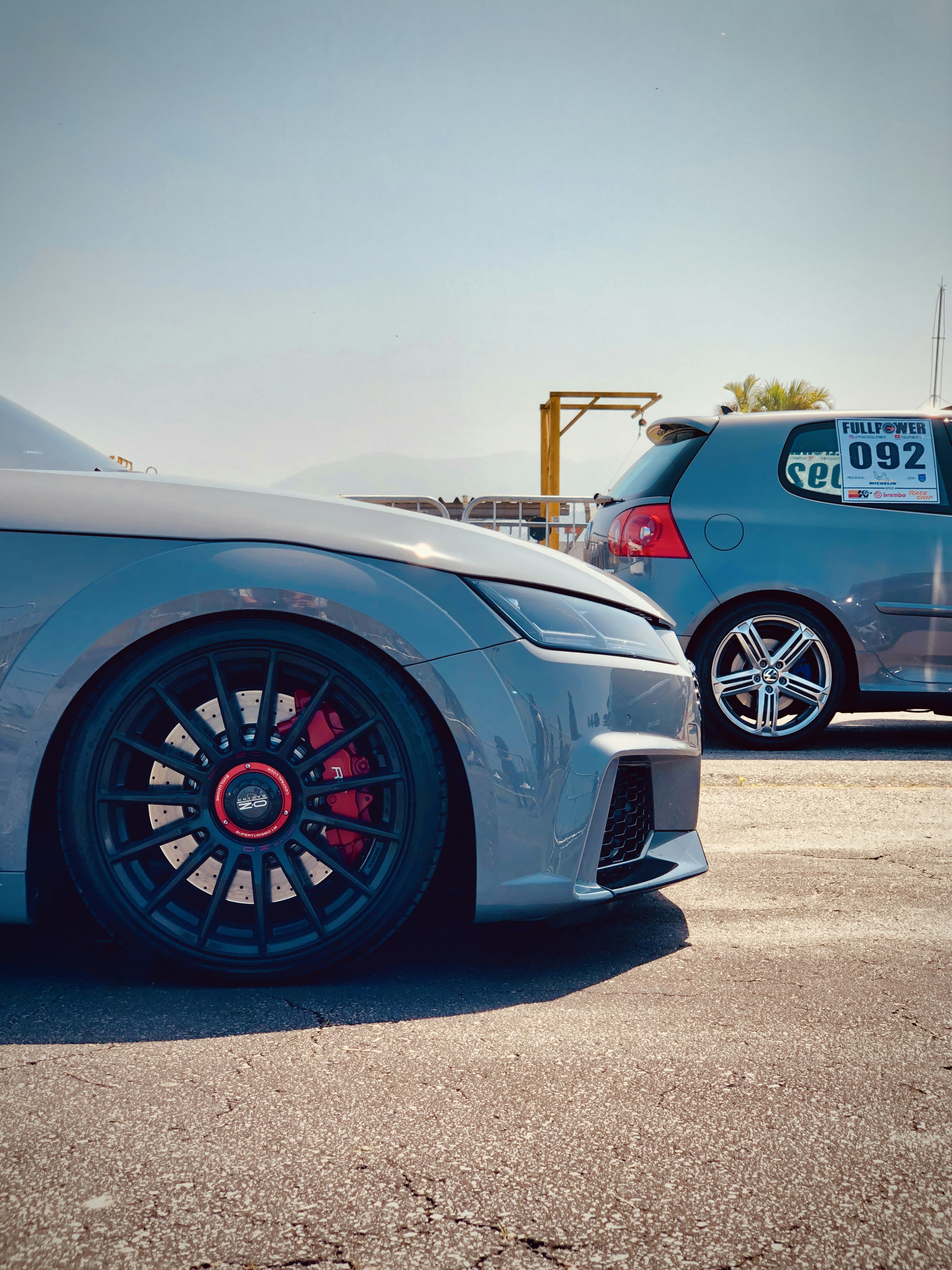 Low-Angle Luxe: Grey Wheel Dominates the Foreground beside a Blue Hatchback