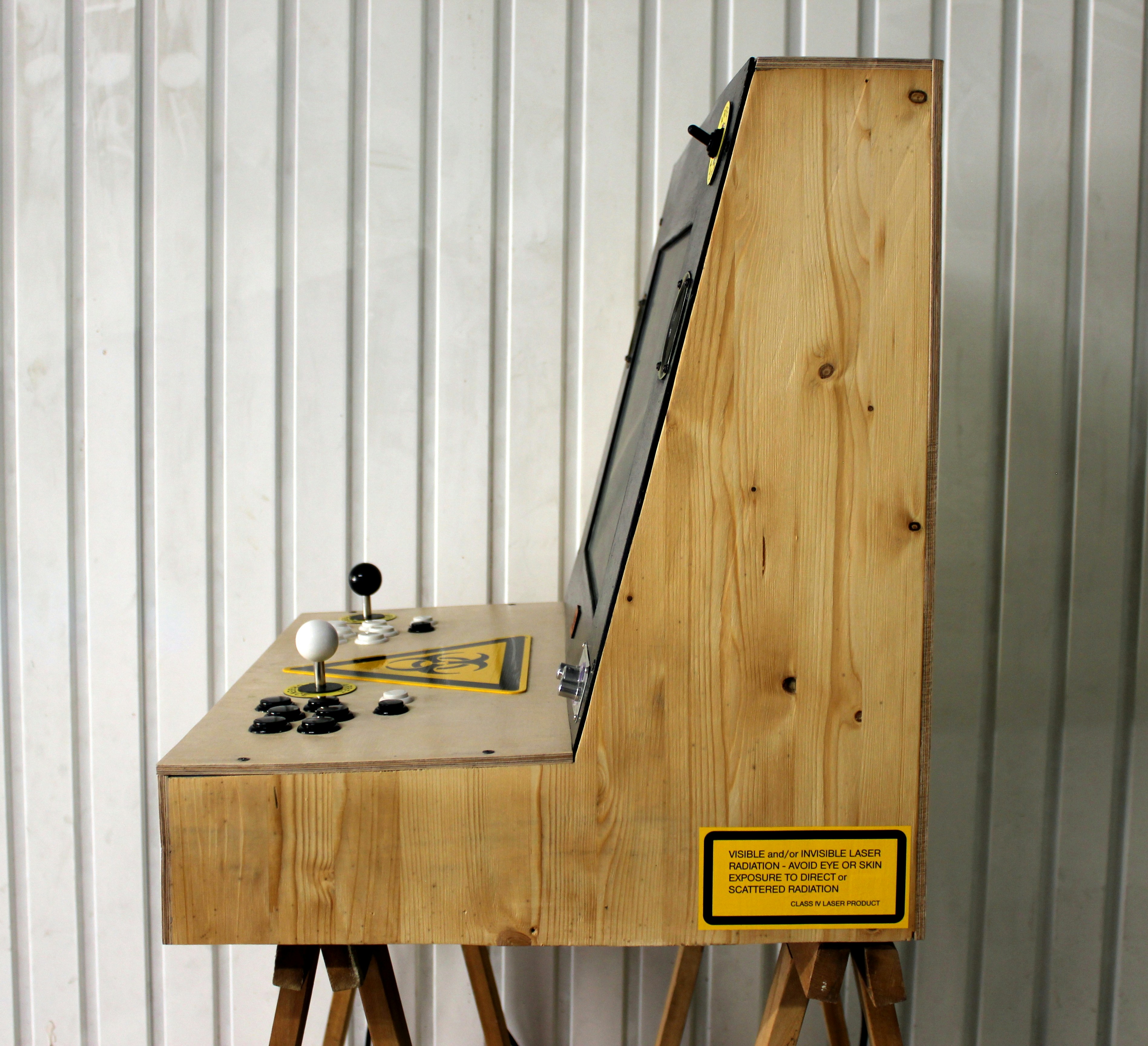 Wooden arcade machine with joystick and buttons set against a corrugated metal backdrop.