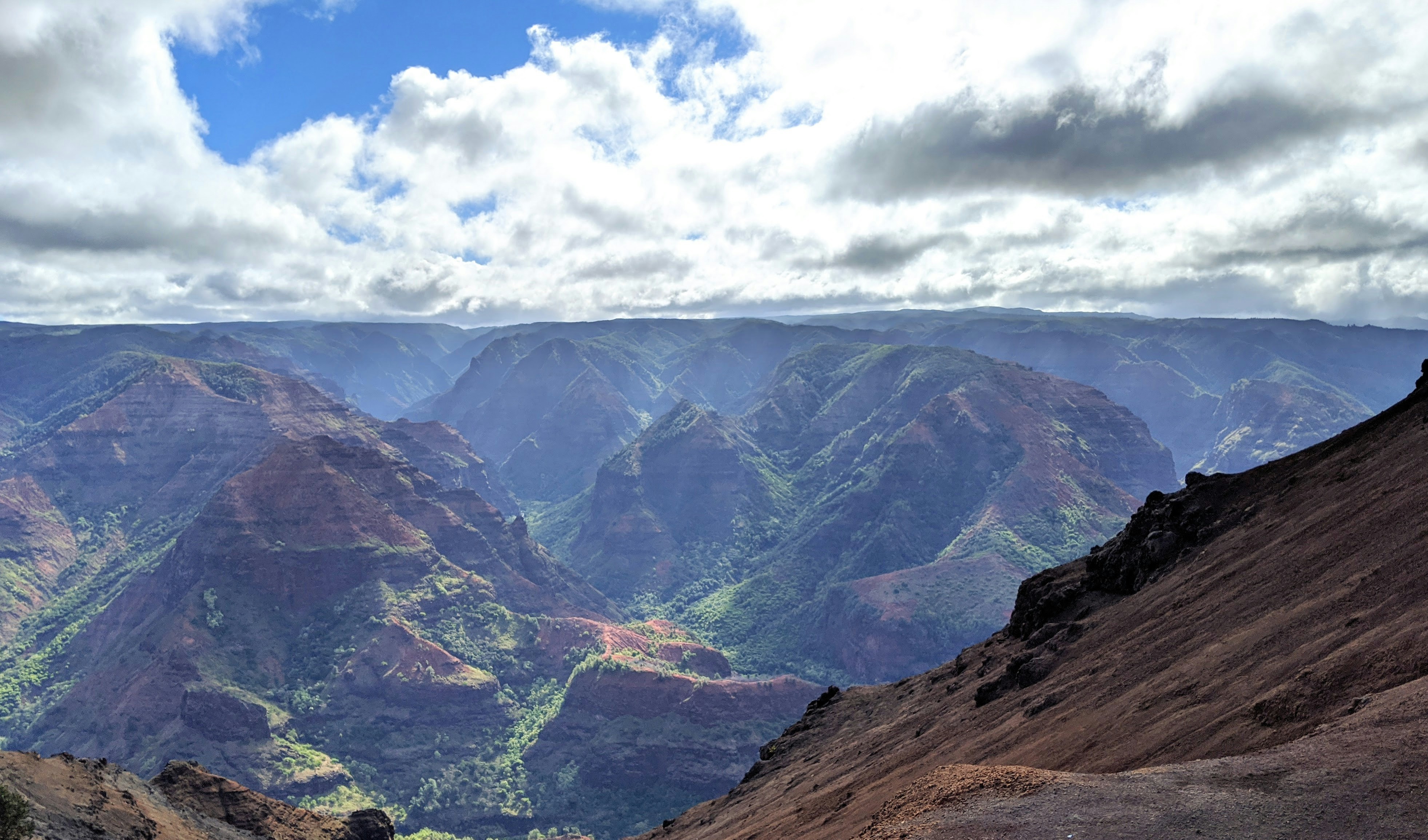 Vast canyon landscape with sunlit ridges and deep shadows under a partly cloudy sky.