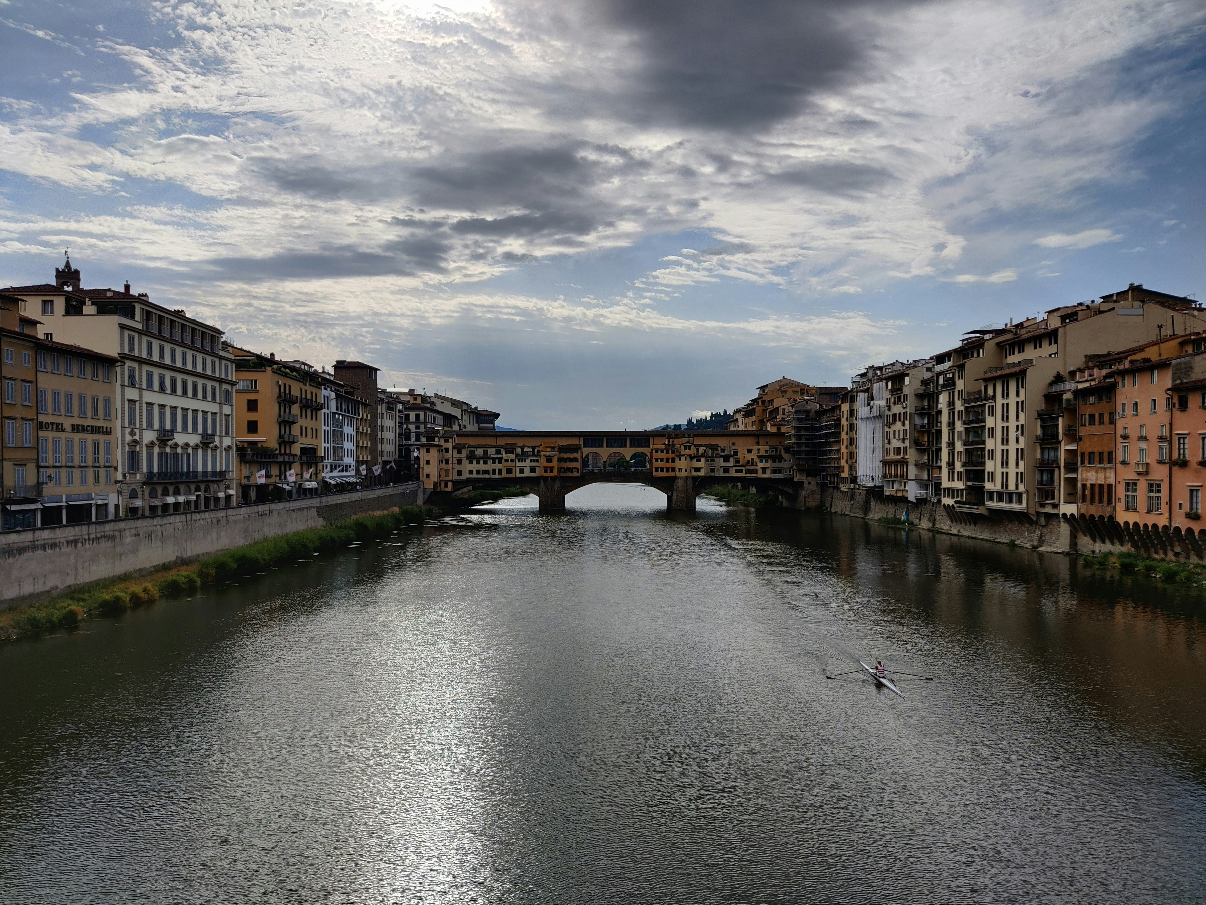 Canoeist gliding on the river beneath the Ponte Vecchio under a dramatic sky.
