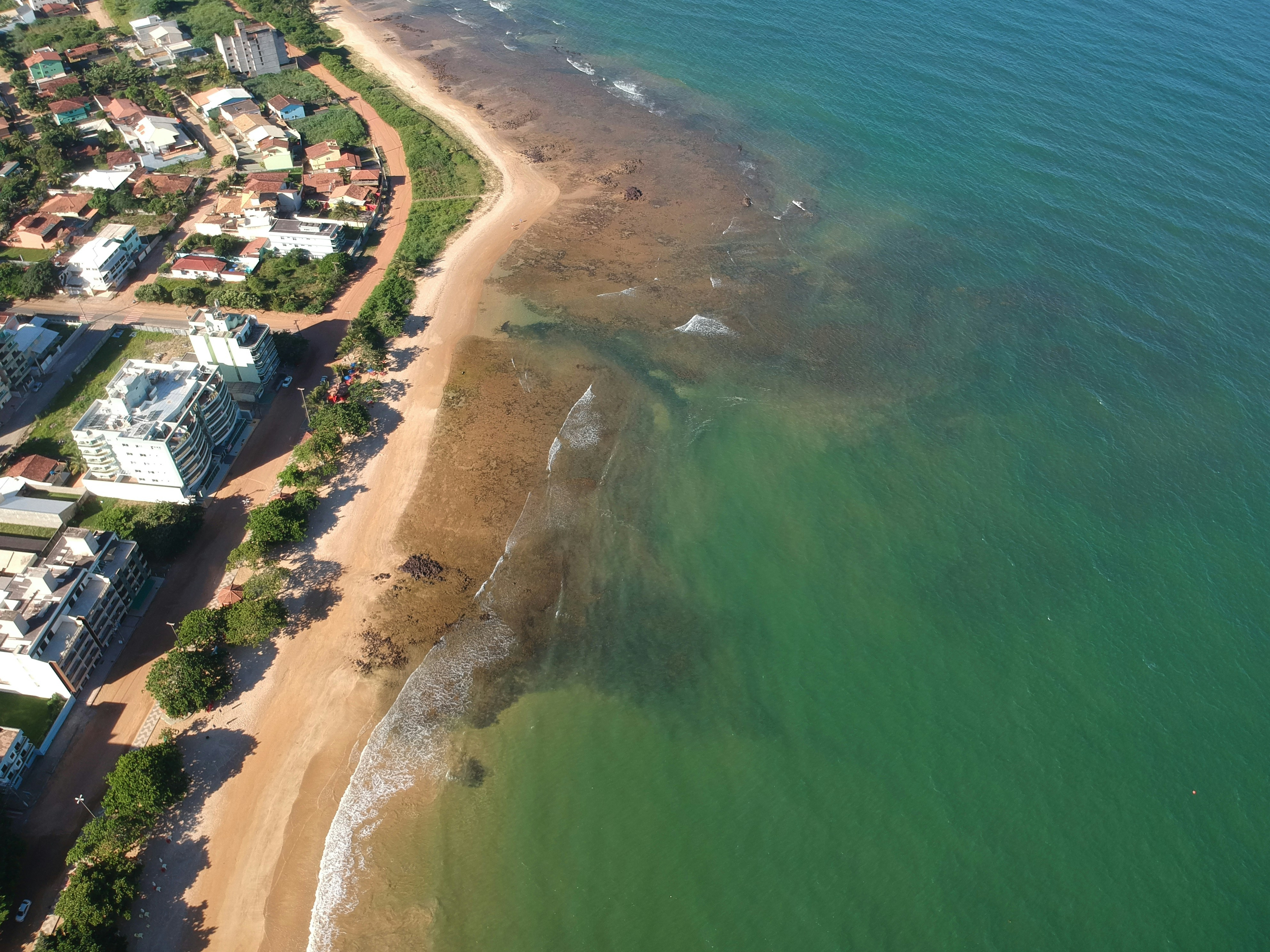 Aerial view of a coastal area with turquoise waters meeting a sandy beach lined with residential buildings.