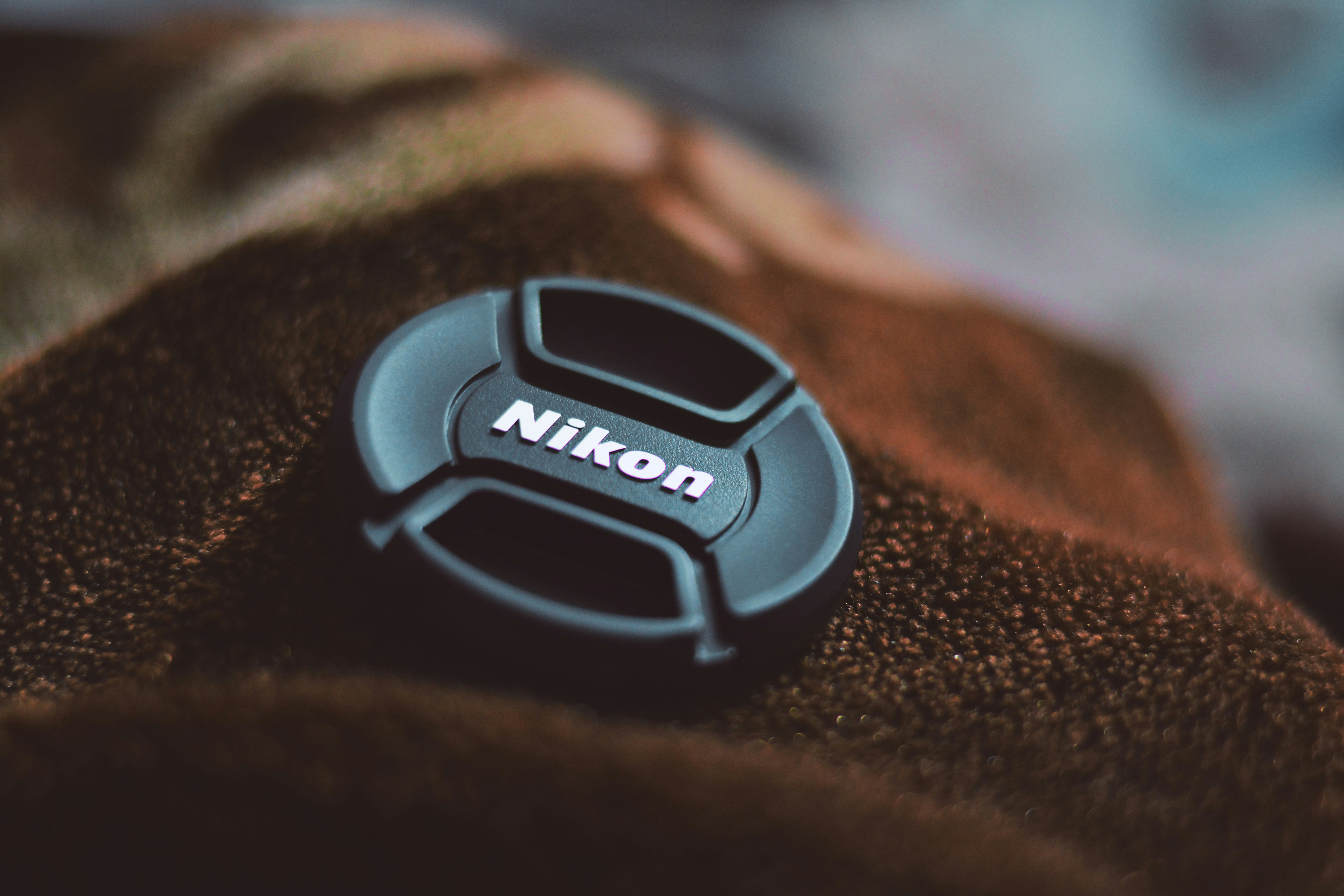 Close-up of a Nikon lens cap resting on a textured surface, showcasing the brand's logo prominently.