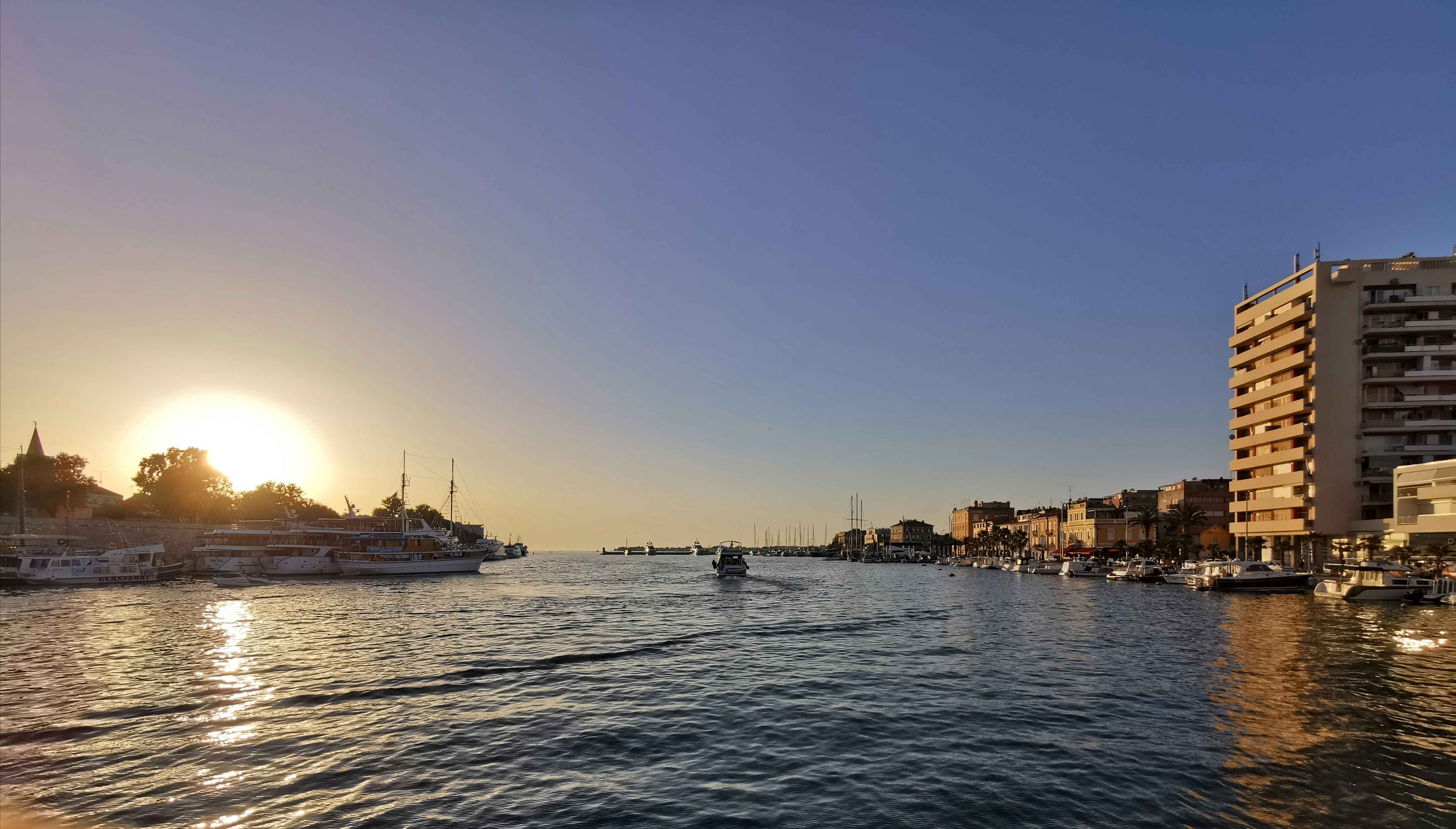 Sunset over a tranquil harbor in Croatia with boats and buildings silhouetted against the evening sky.