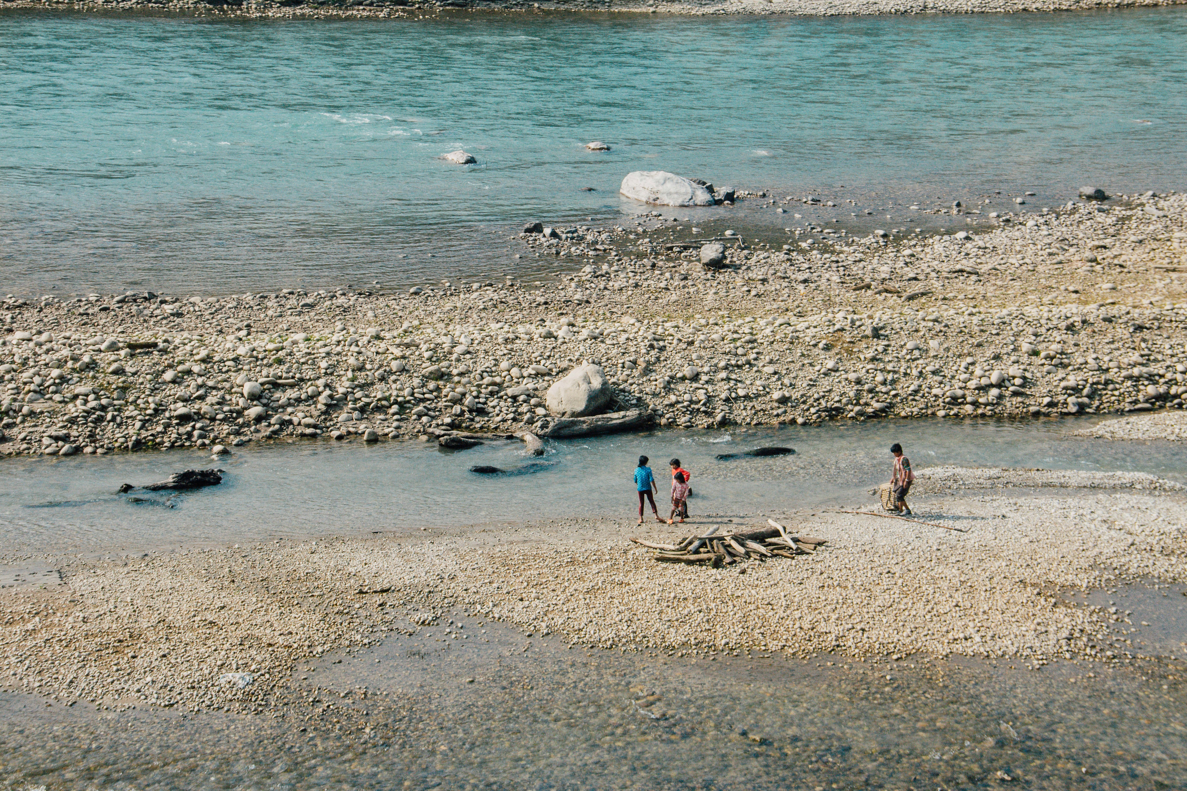 Group of people standing on a rocky riverbank with turquoise water flowing nearby.