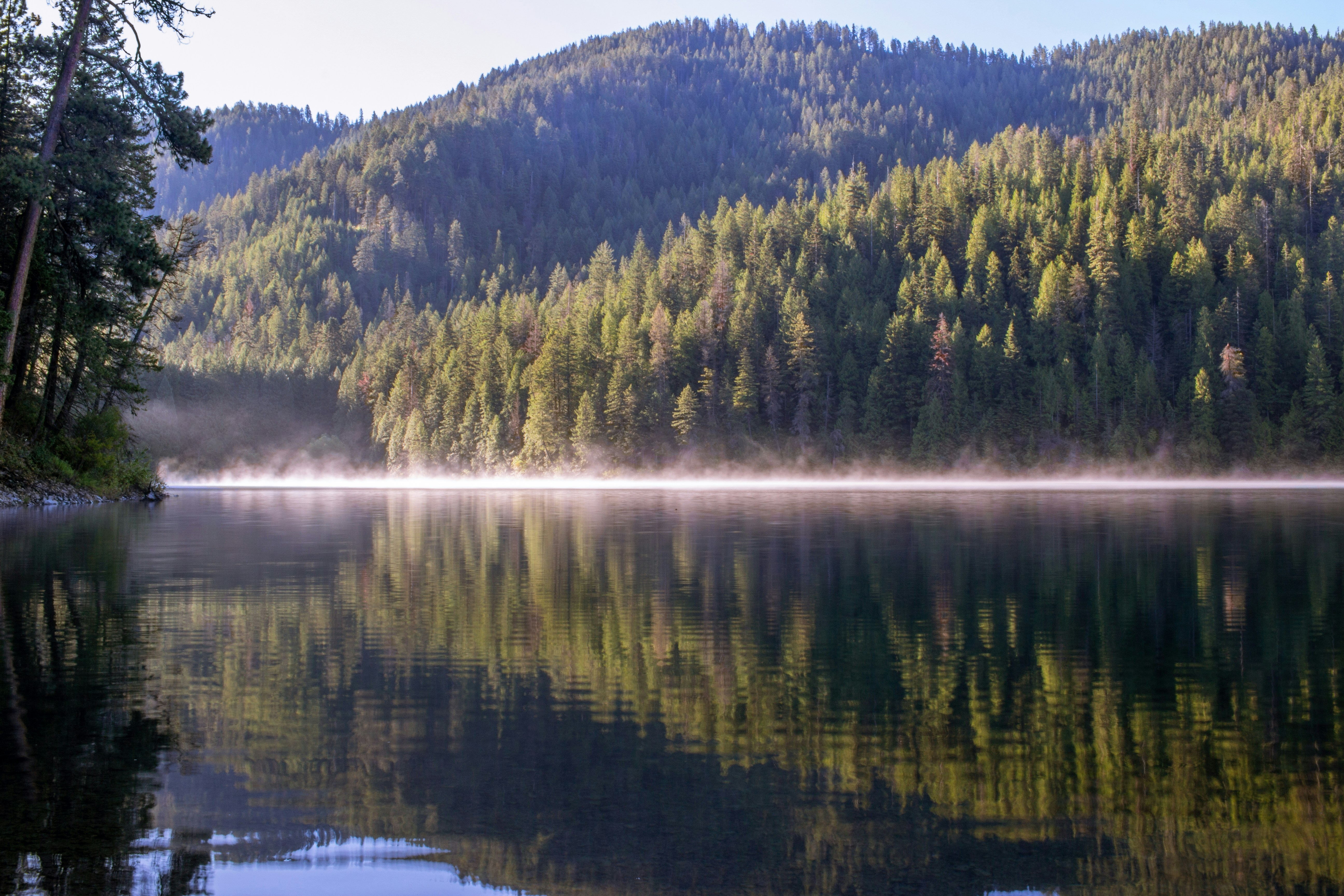 Calm lake reflecting forested hills under a soft morning mist.