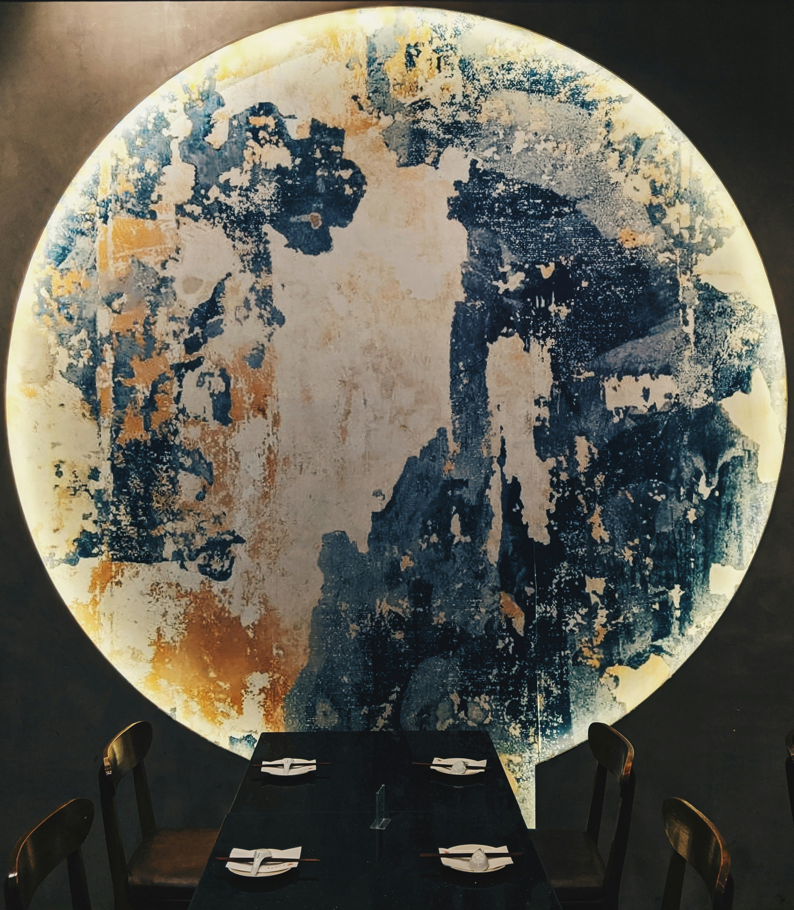 Circular painting with peeling textures forms a warm halo behind a dark dining table.