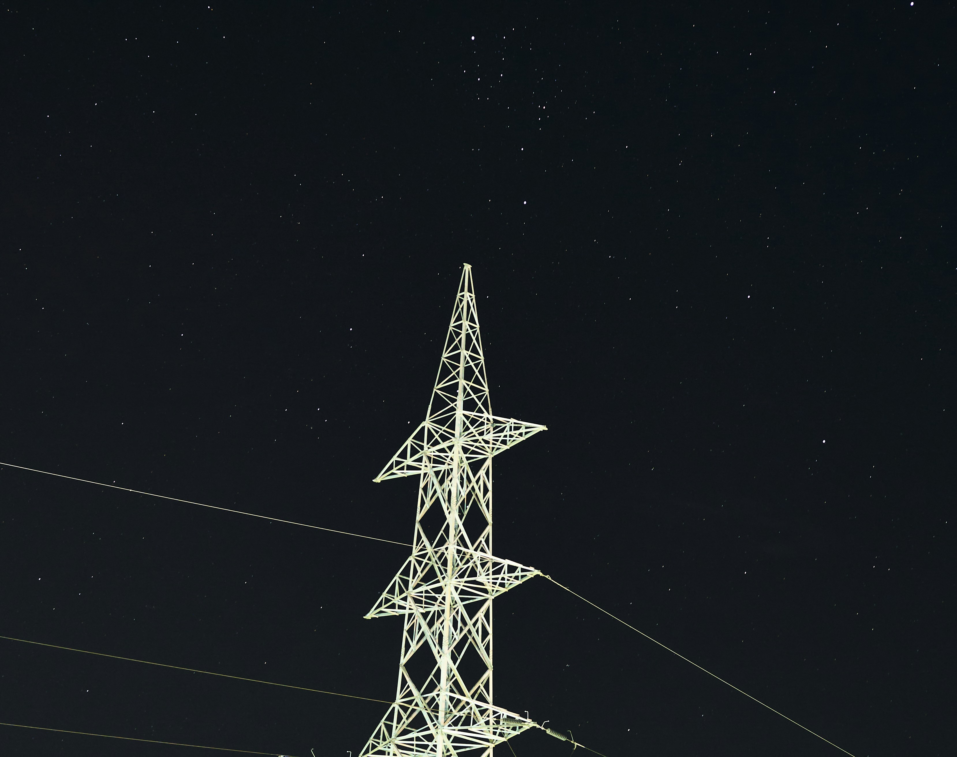 A towering electricity pylon stands against a backdrop of twinkling stars, highlighting the contrast between man-made structures and the vast cosmos above.