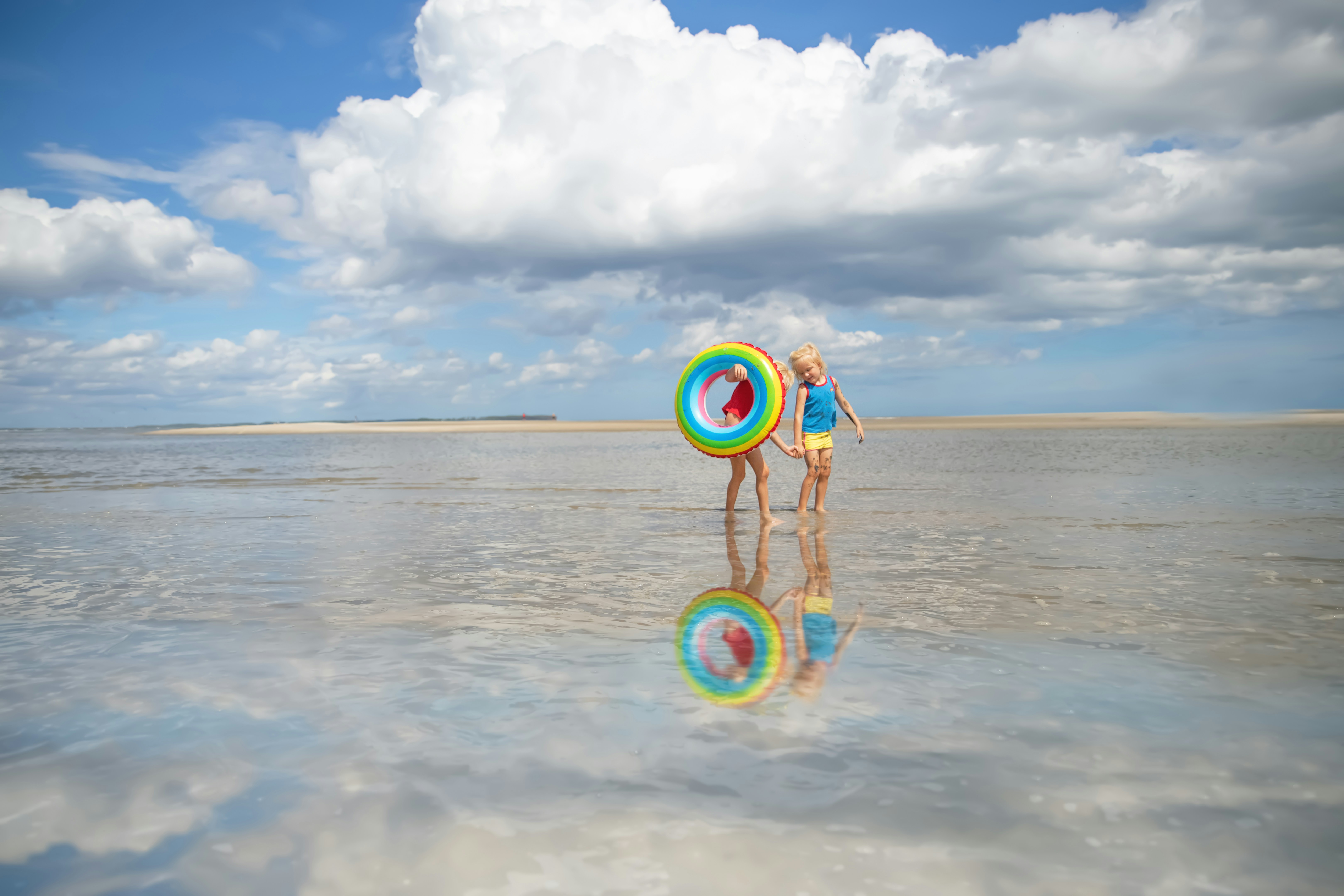 Child in a white dress holds a colorful bicycle on a tranquil beach with clear skies.