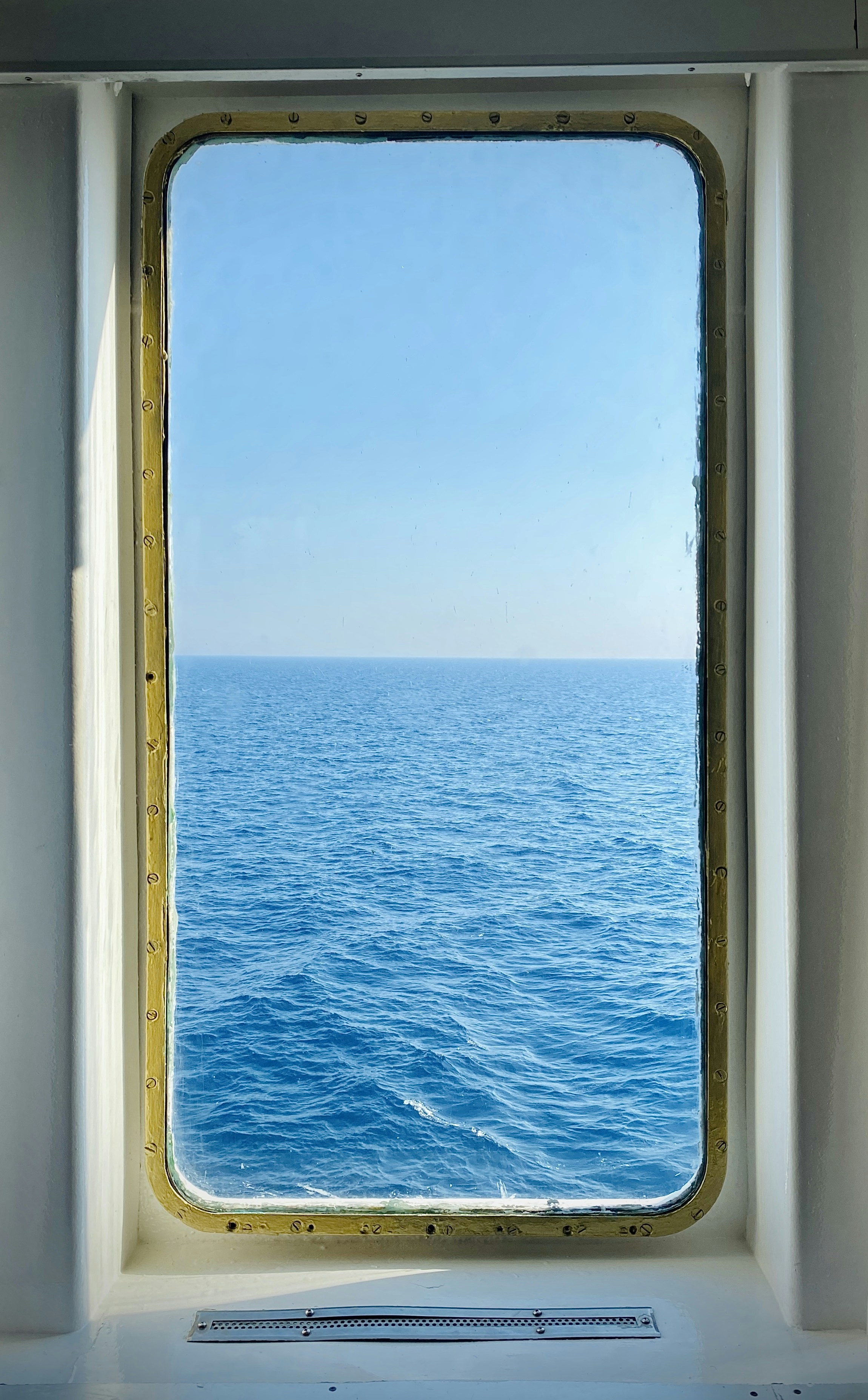 Clear view of the ocean through a ship's window, showcasing the endless blue waters and a serene sky. 
