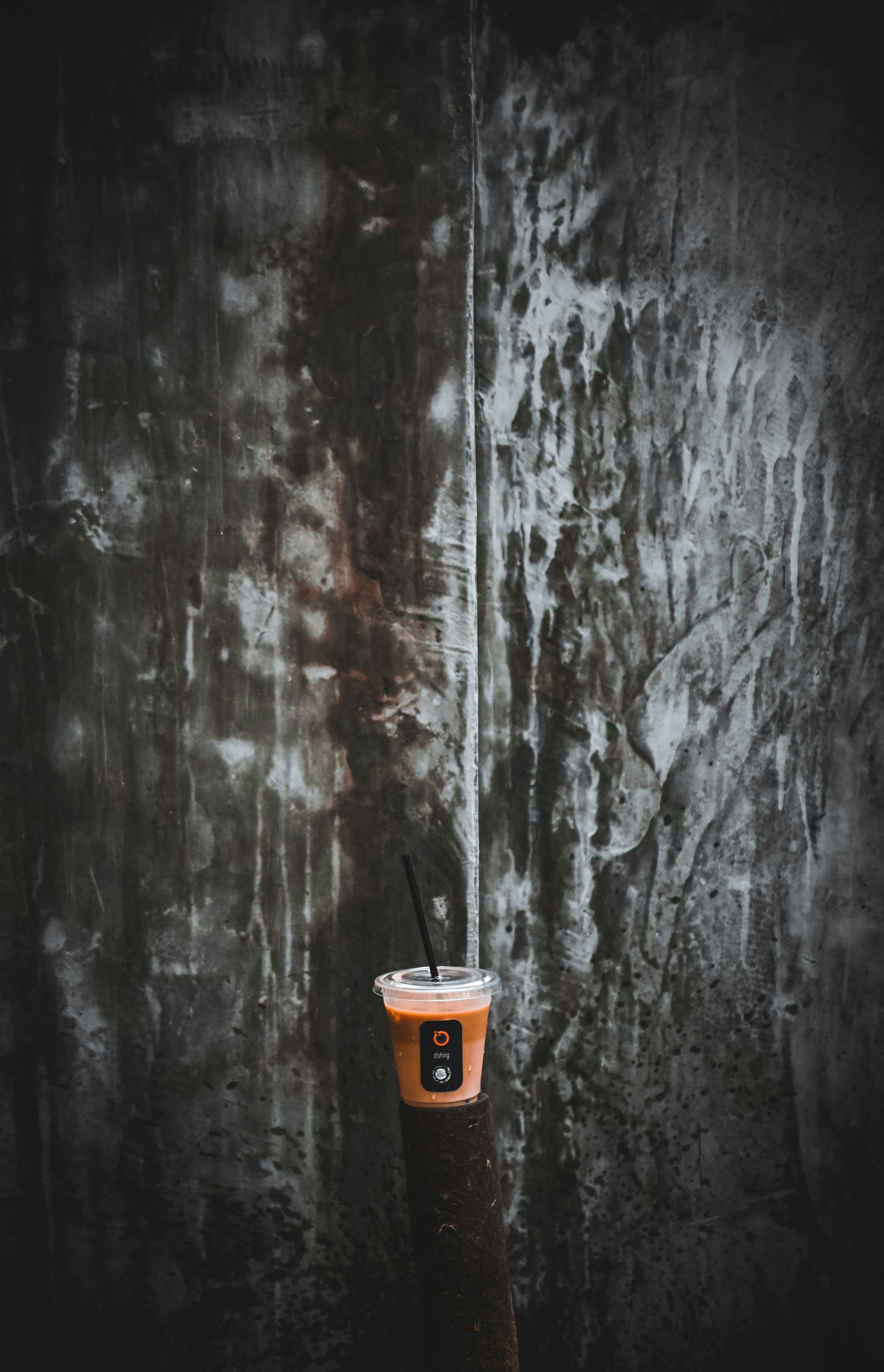 Rust and Quiet: A Lone Orange Cup Perched on a Weathered Pipe in a Shadowed Industrial Wall