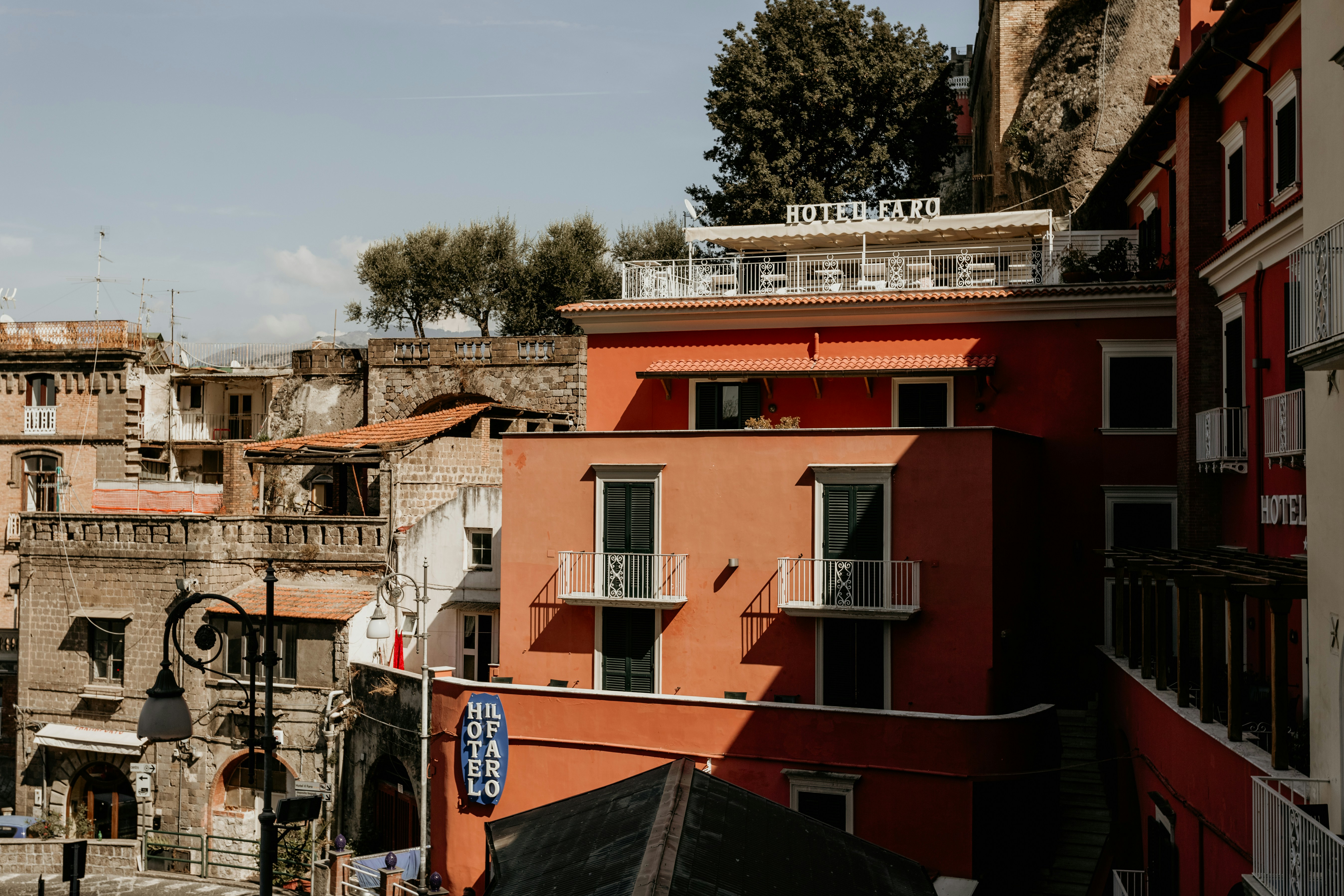 Colorful buildings with sunlit terraces and a tree-lined backdrop in a quaint village.