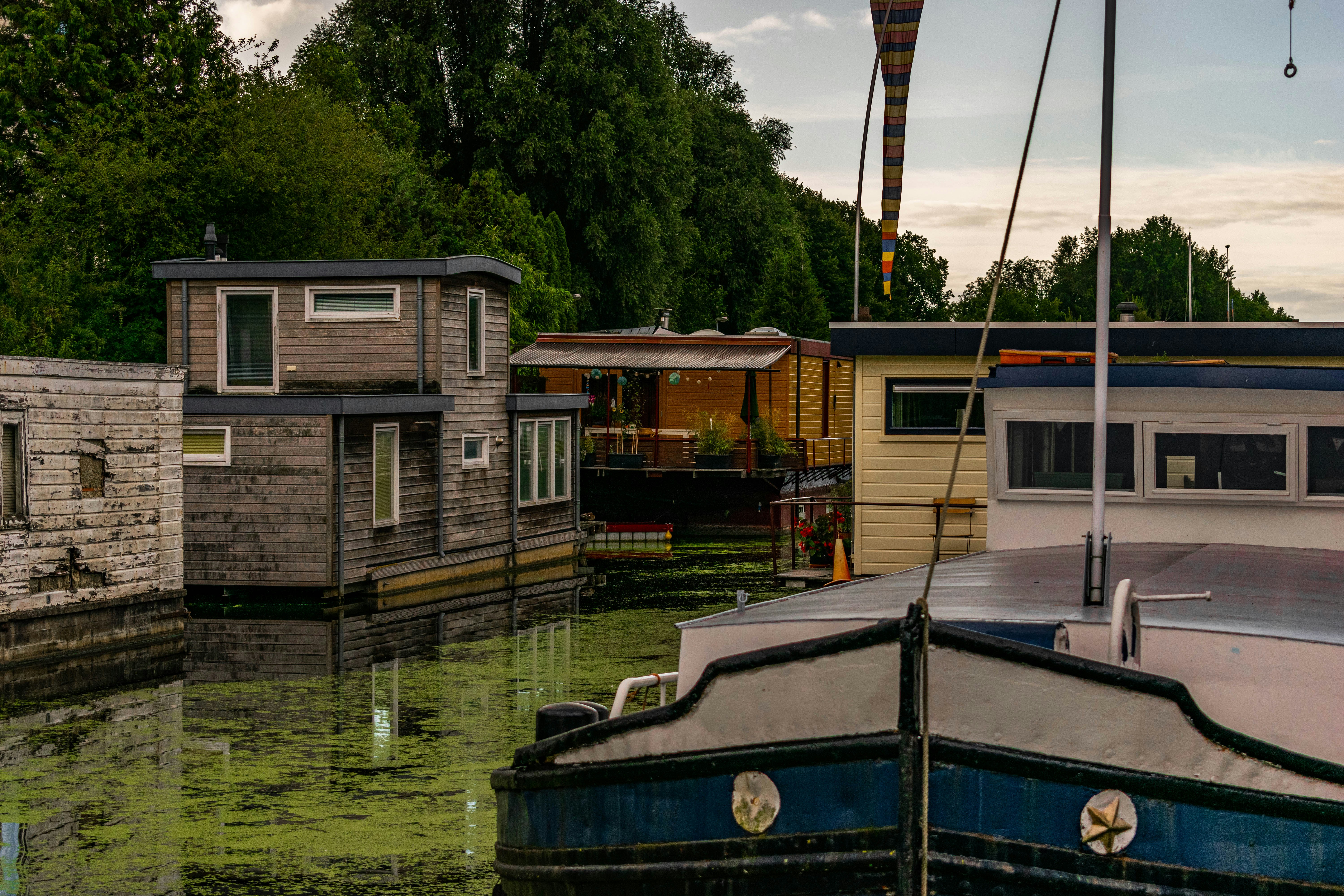 Blue and brown wooden boat anchored near eclectic houseboats on a tranquil waterway.