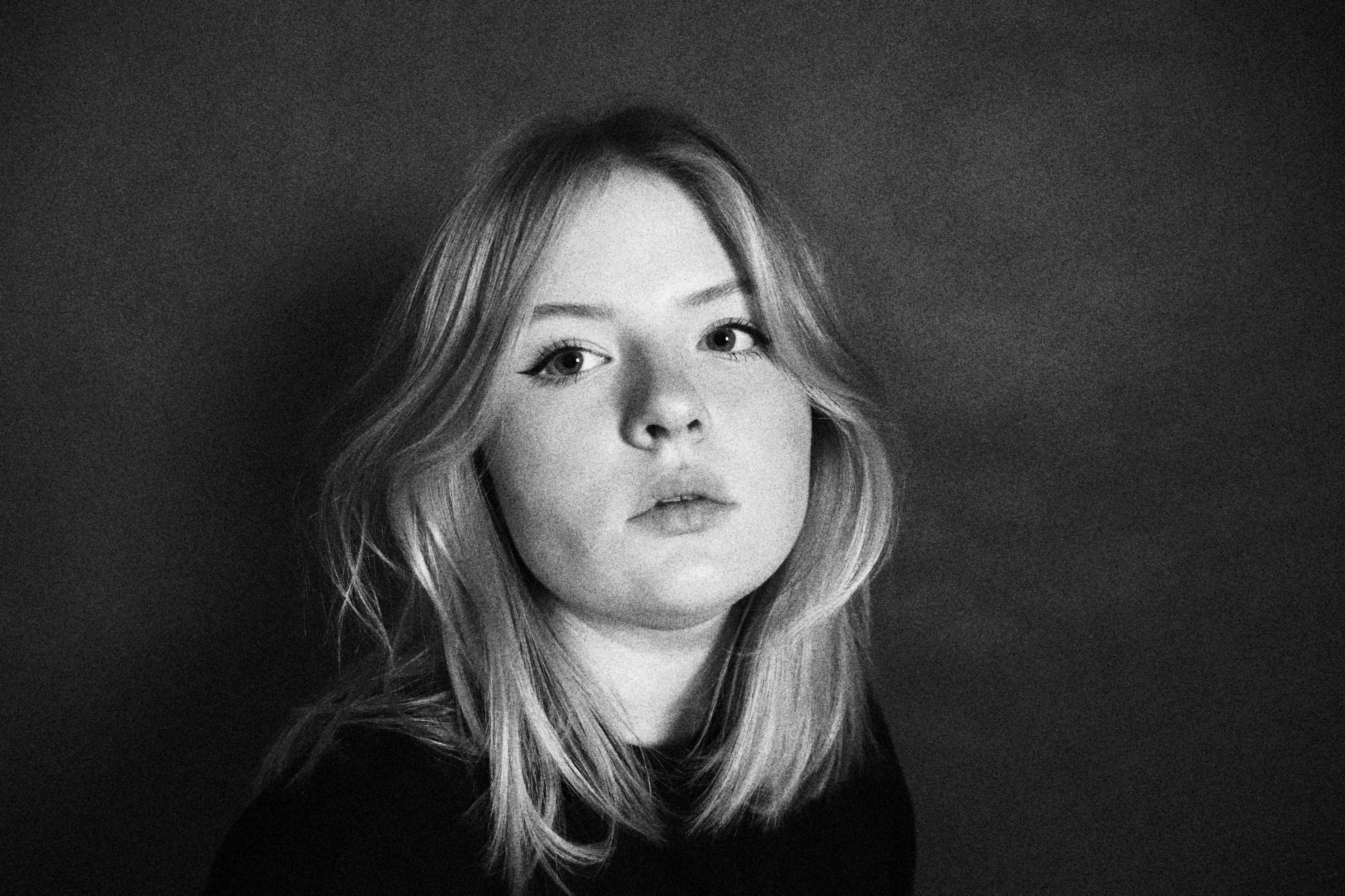 Black and white portrait of a young woman with soft features and a contemplative expression against a muted background.