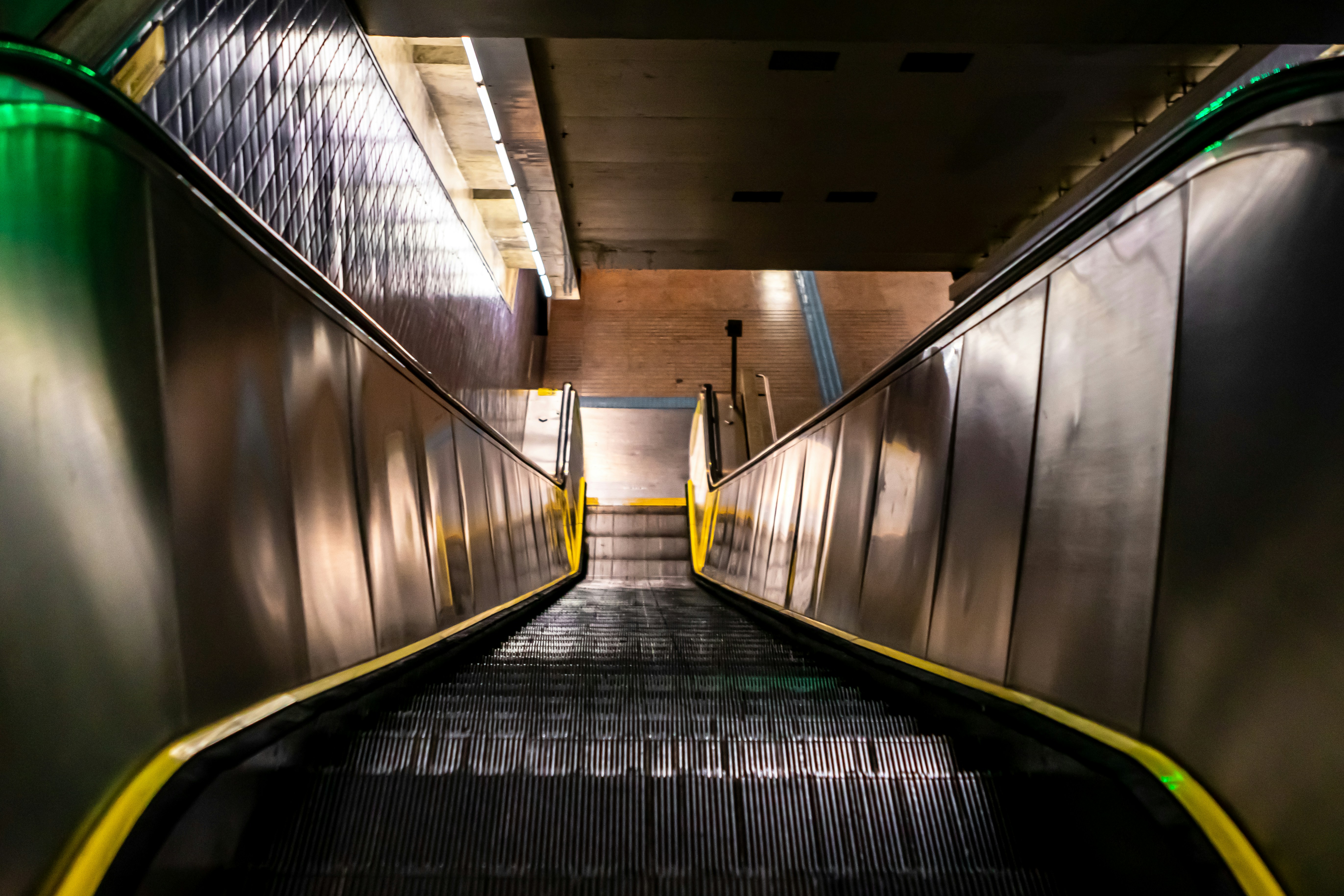 Underground escalator bathed in warm artificial light, leading to a metallic corridor.