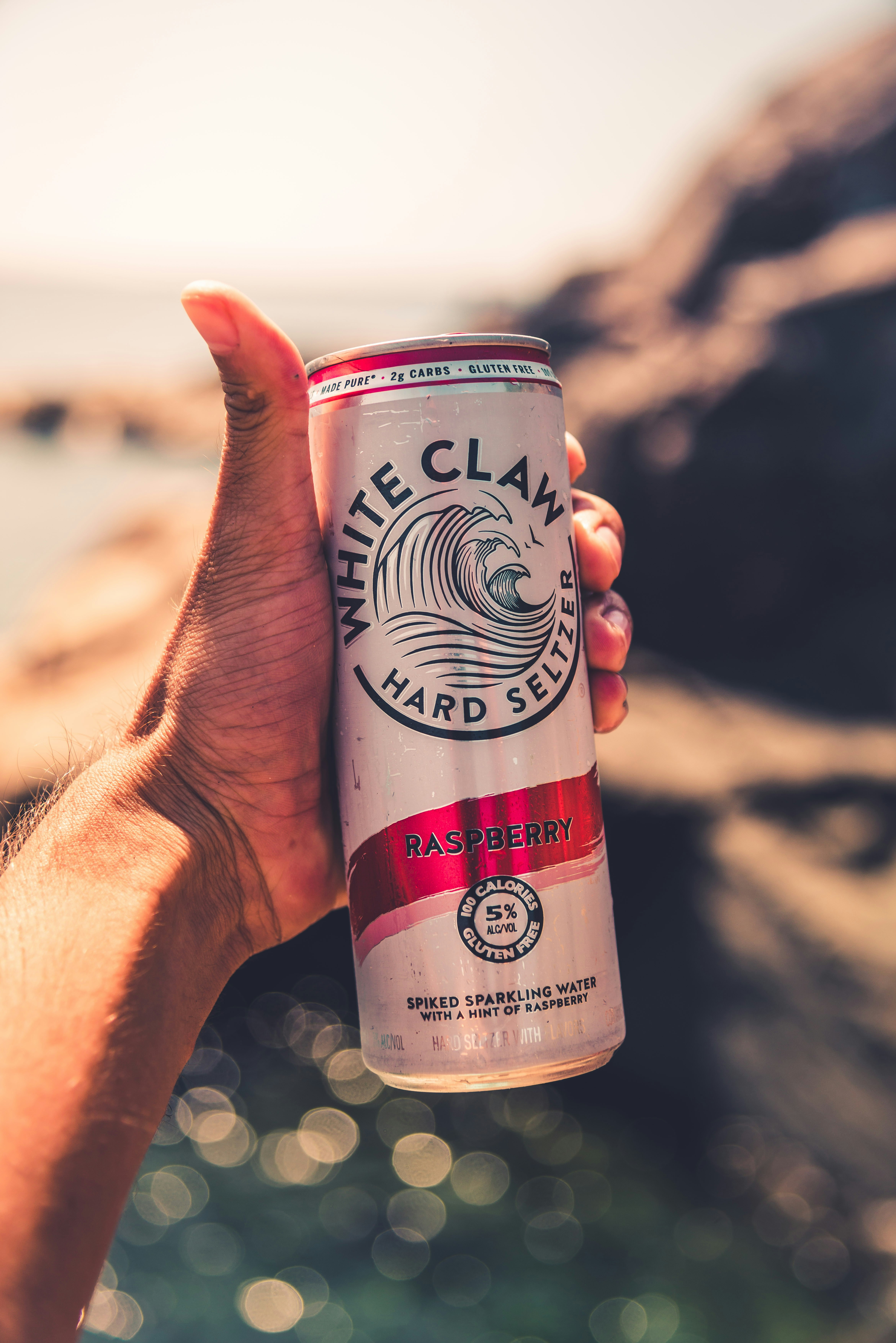Citrus Chill: Handheld can of Raspberry White Claw in sunlit seaside glow