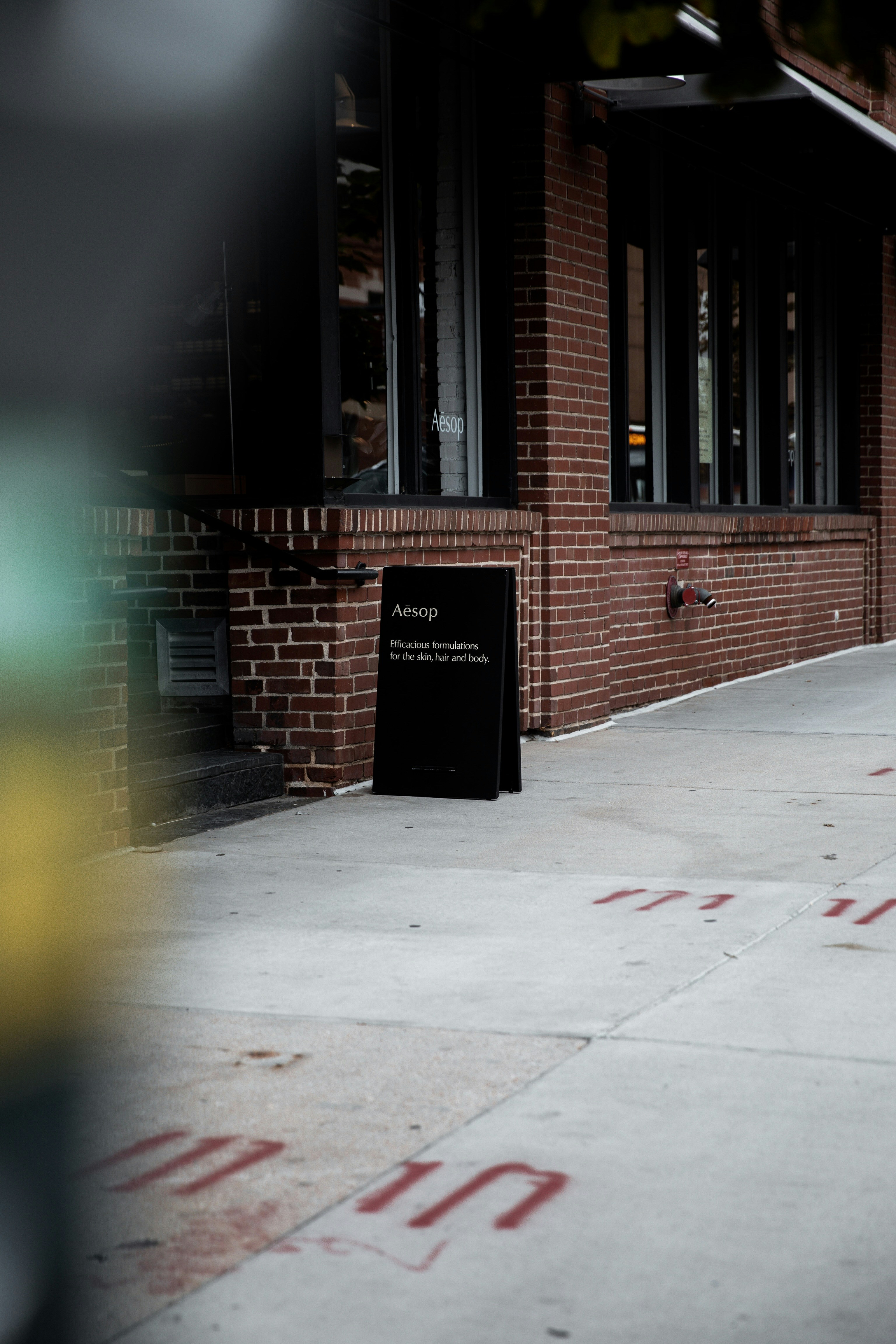 Aesop storefront showcasing minimalist branding against a brick wall, inviting passersby to explore their skincare offerings.