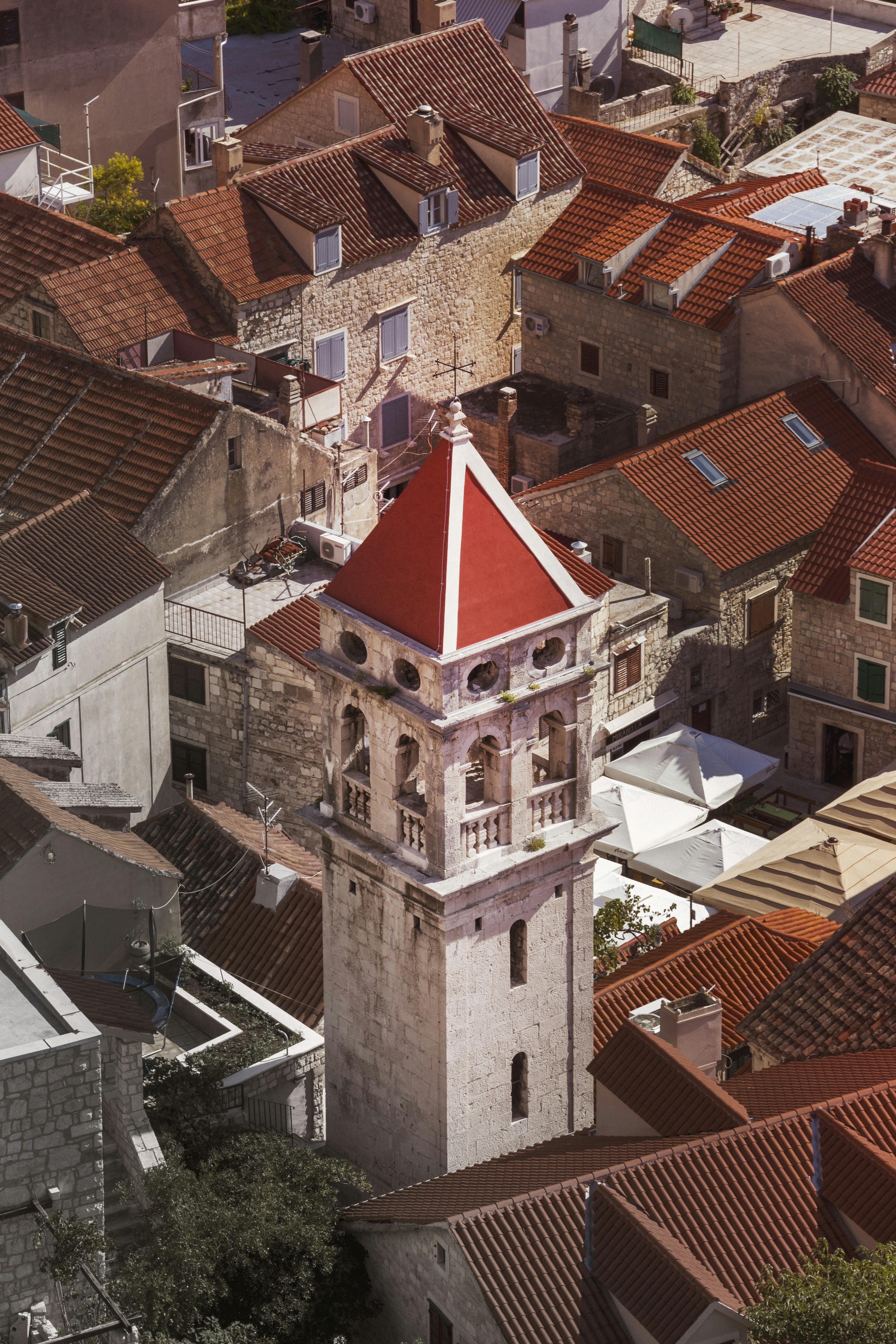 A stone bell tower with a striking red roof rises above a cluster of traditional buildings, showcasing the rich architectural heritage of the area.