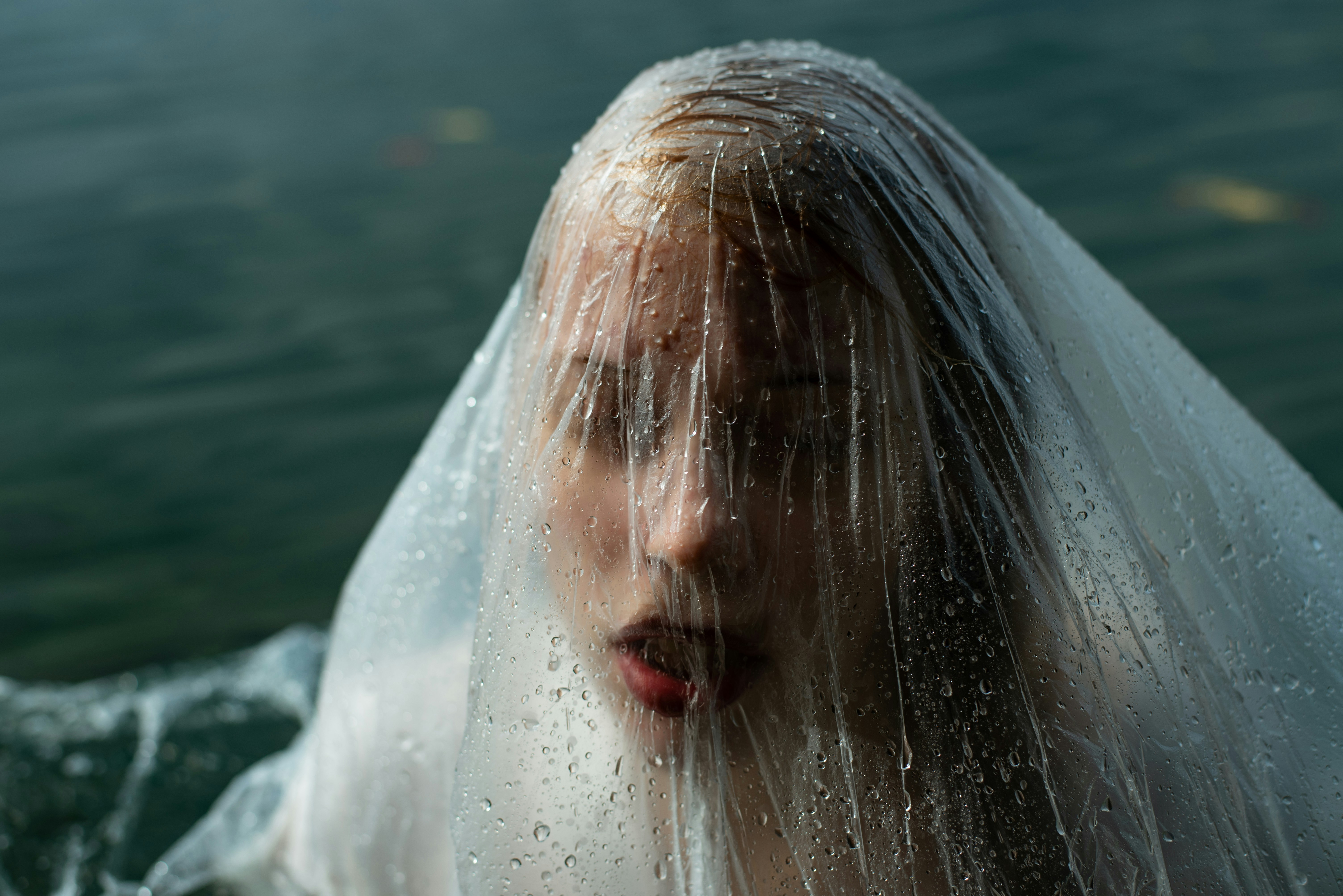 Person partially submerged in water with a translucent veil covering their face.