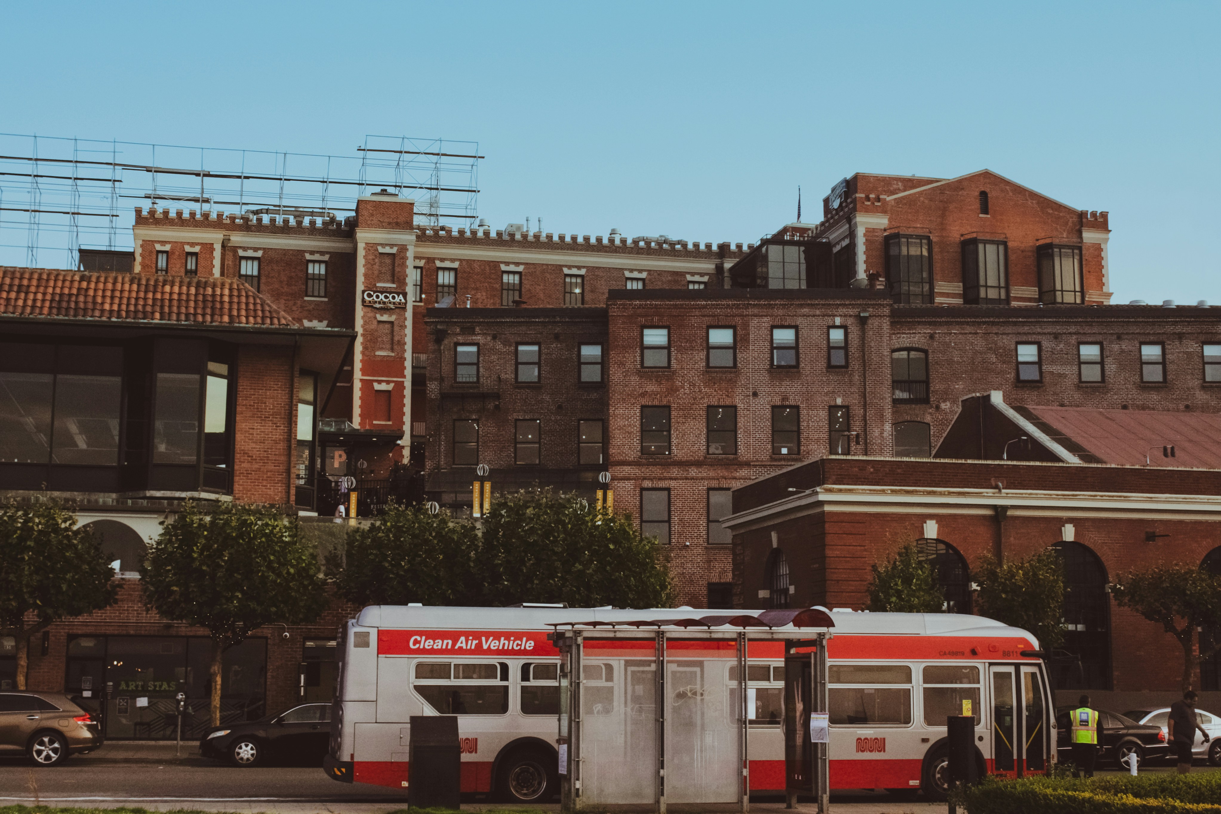 A clean air bus parked in front of a blend of vintage and modern buildings, showcasing urban life and public transport. The scene captures the essence of city commuting.