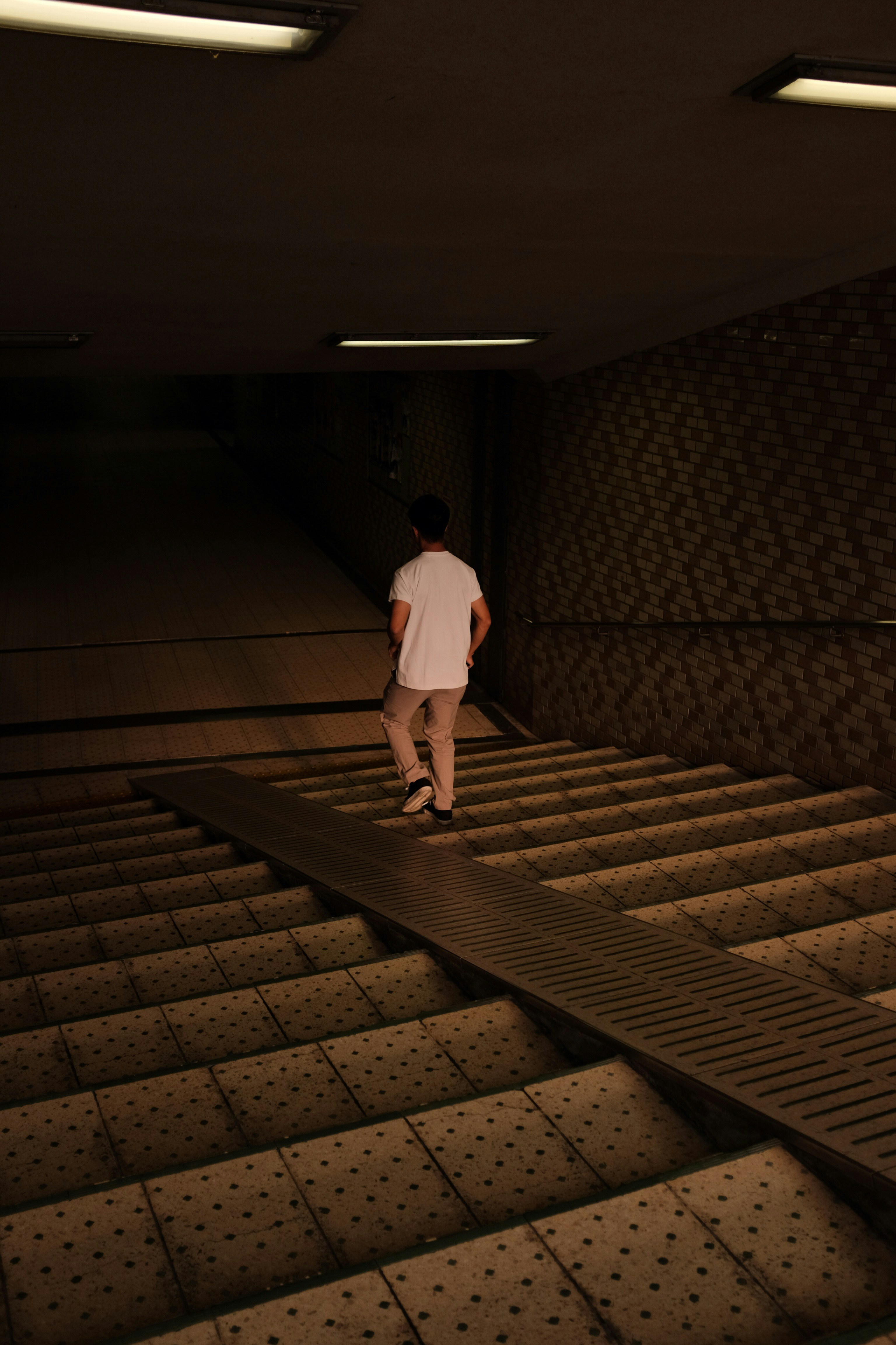 Midnight Ascent: A lone traveler in a shadowed subway stairwell
