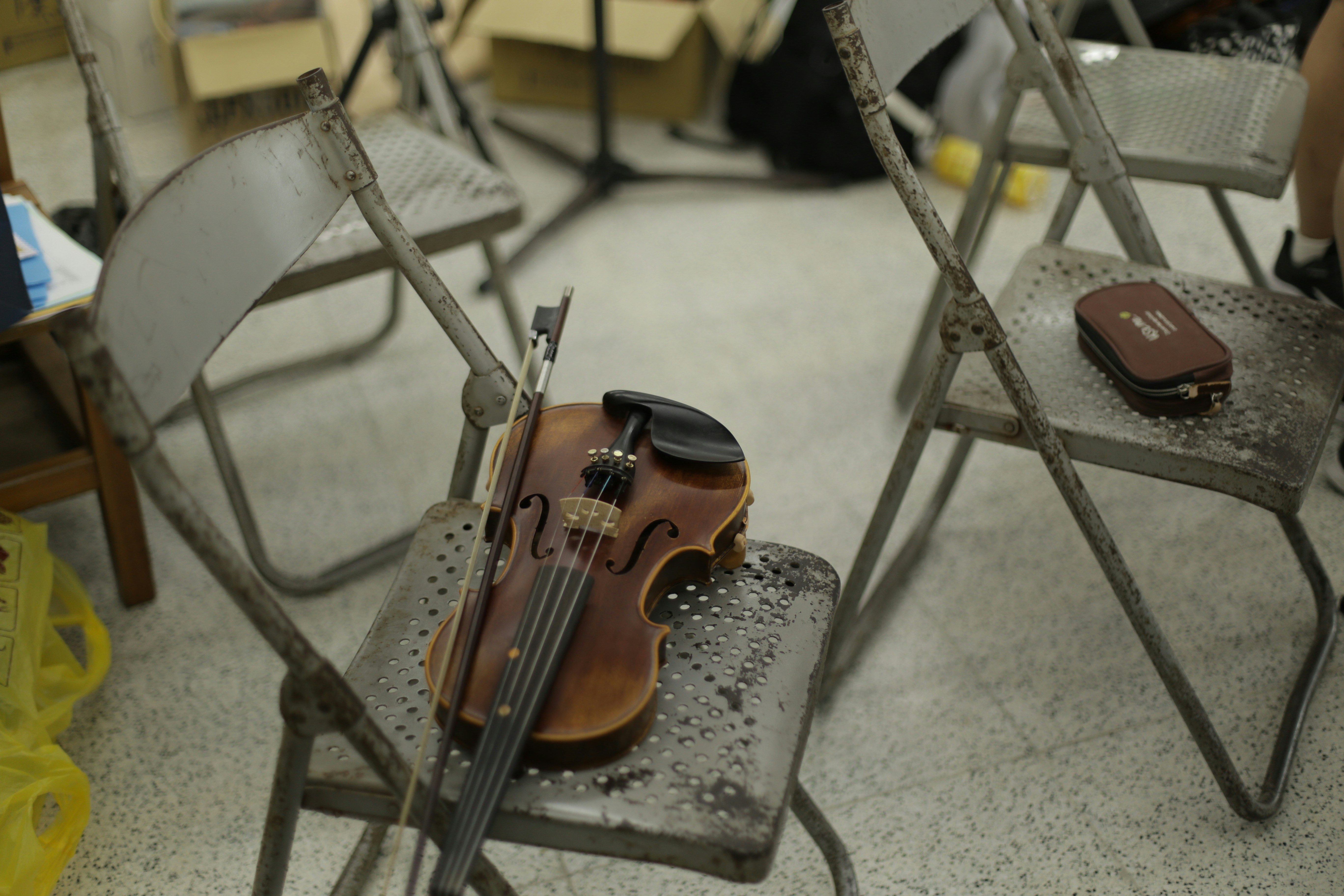 An abandoned violin rests on a weathered folding chair, surrounded by a cluttered space, hinting at a moment of pause in a musical journey.