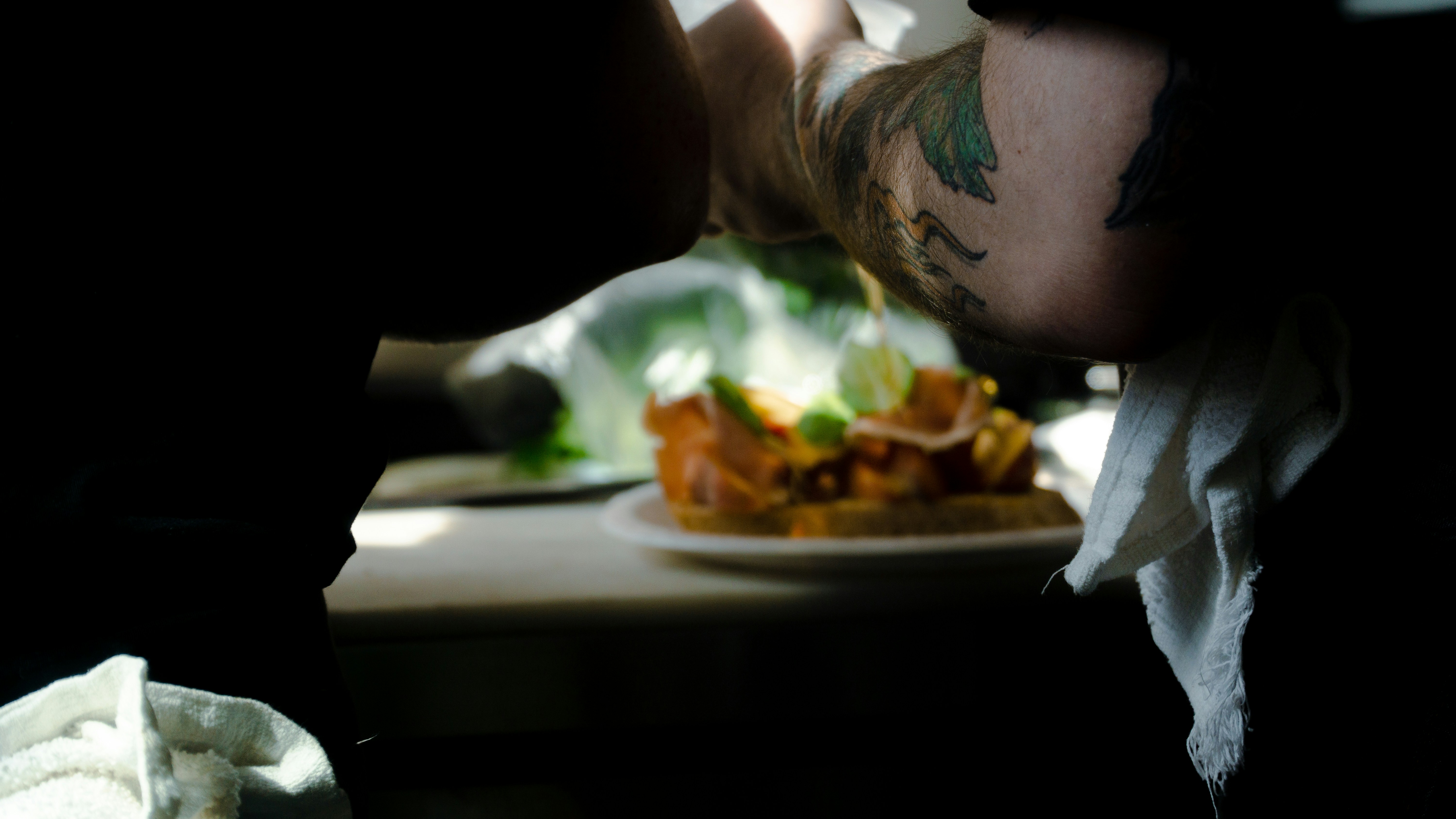 Ink and Appetite: A tattooed forearm hovers over a loaded sandwich