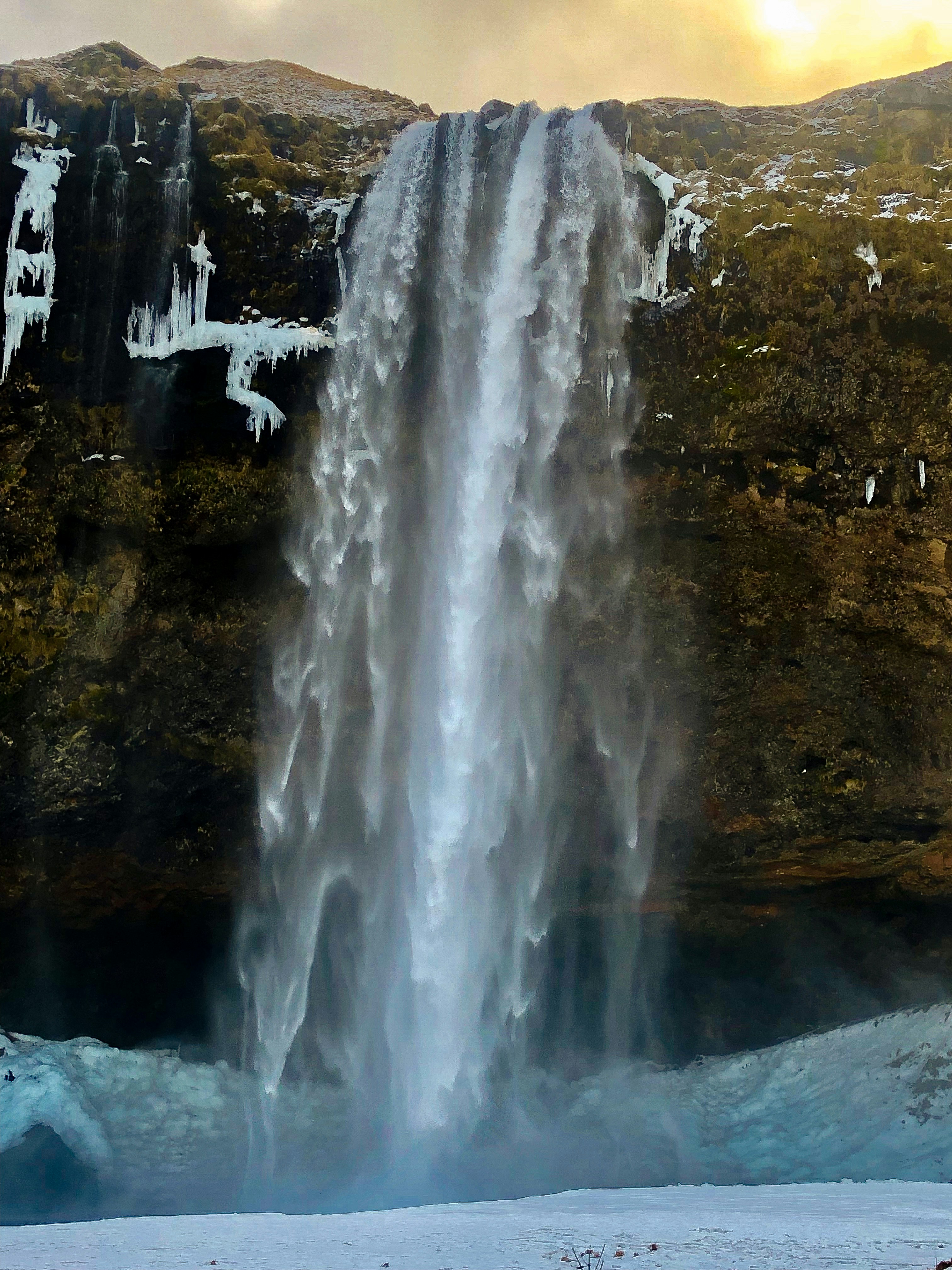 Majestic waterfall cascading down rocky cliffs, surrounded by icy formations and a serene winter landscape.