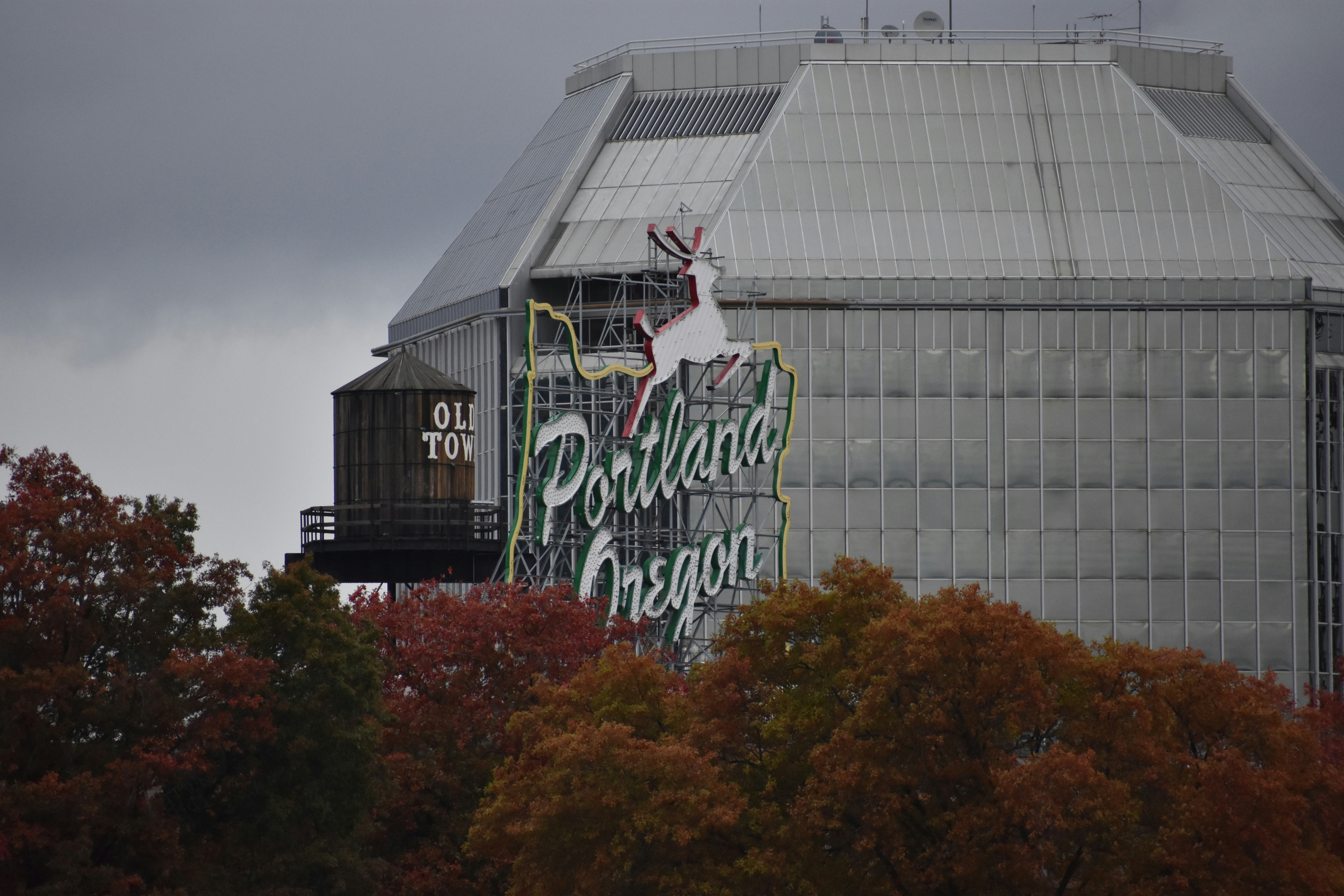 Historic neon sign atop a building surrounded by autumn foliage under a cloudy sky.