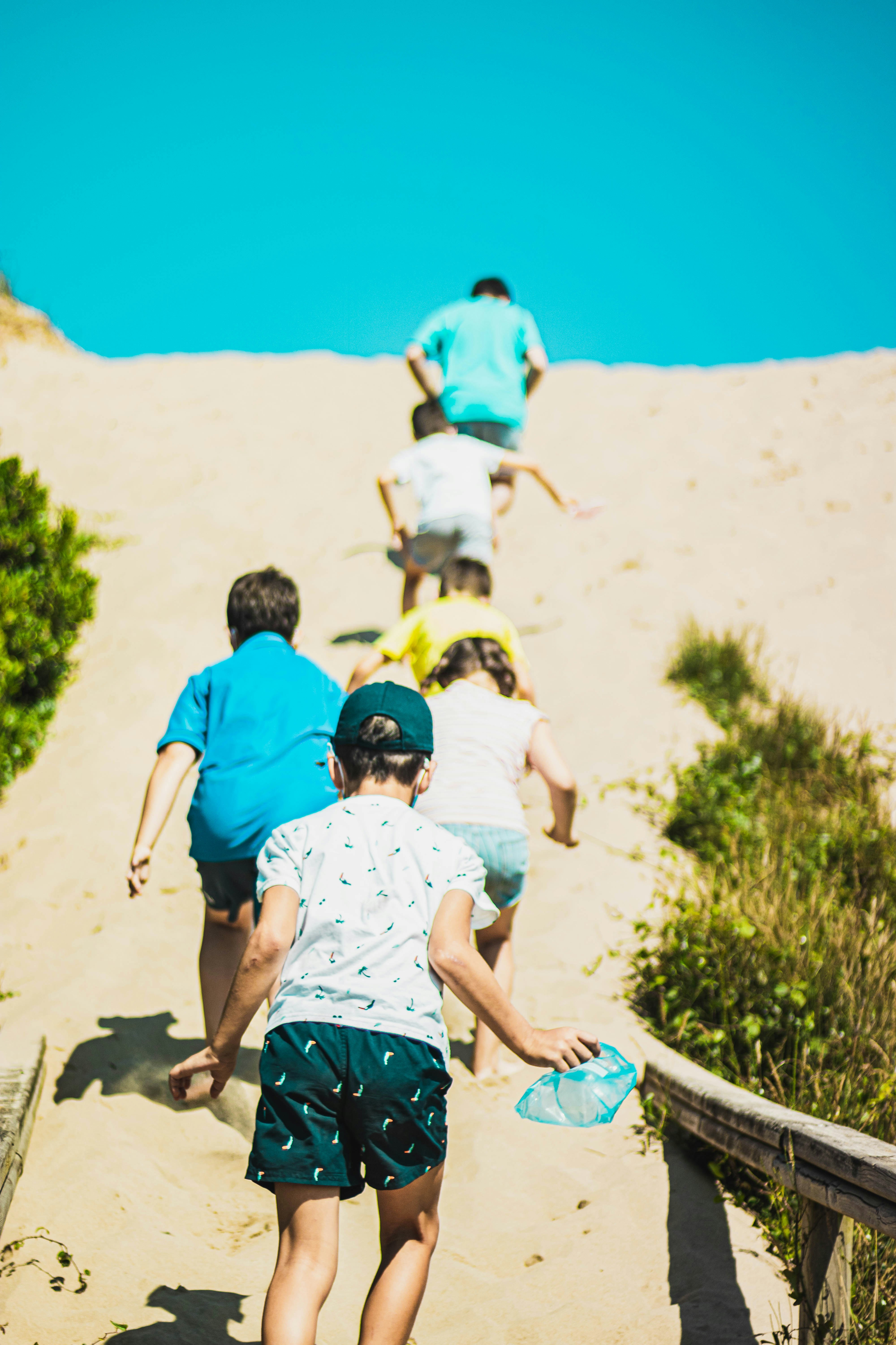 Children climbing a sunlit sand dune under a vibrant blue sky.