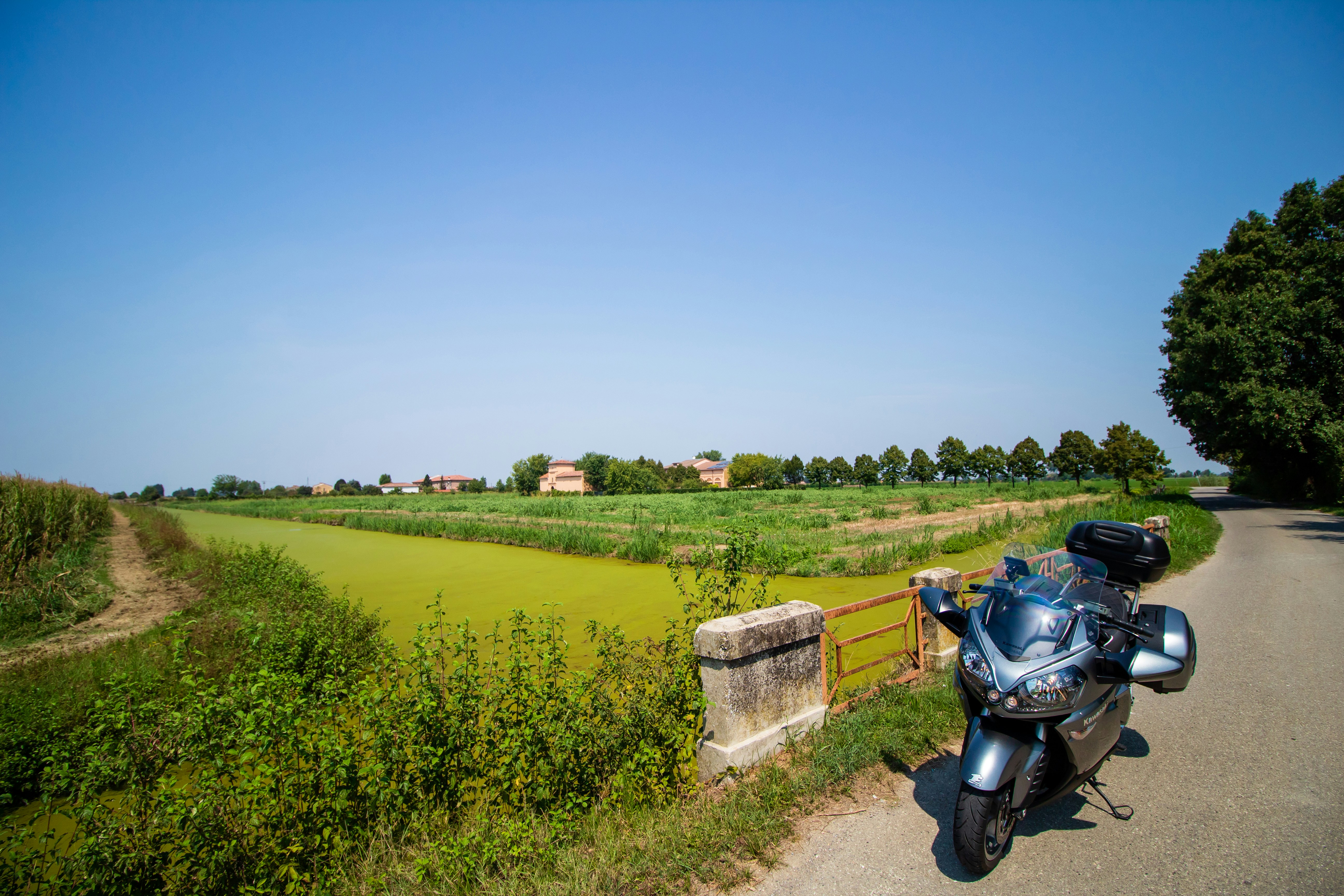 Canal-side Curves: A Silver Motorcycle Pauses on a Sunlit Country Road
