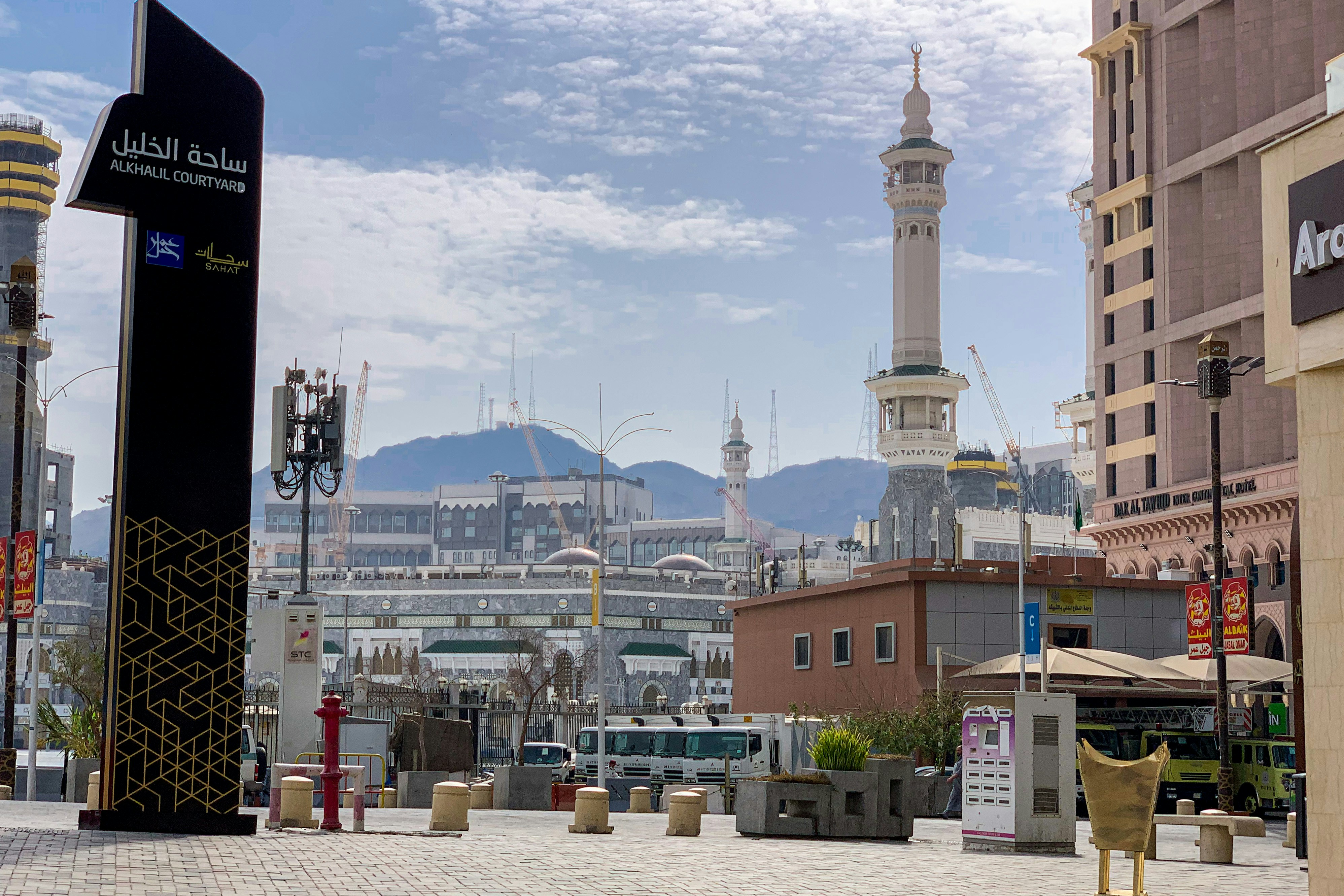 Minarets and modern buildings under a partly cloudy sky with distant mountains.