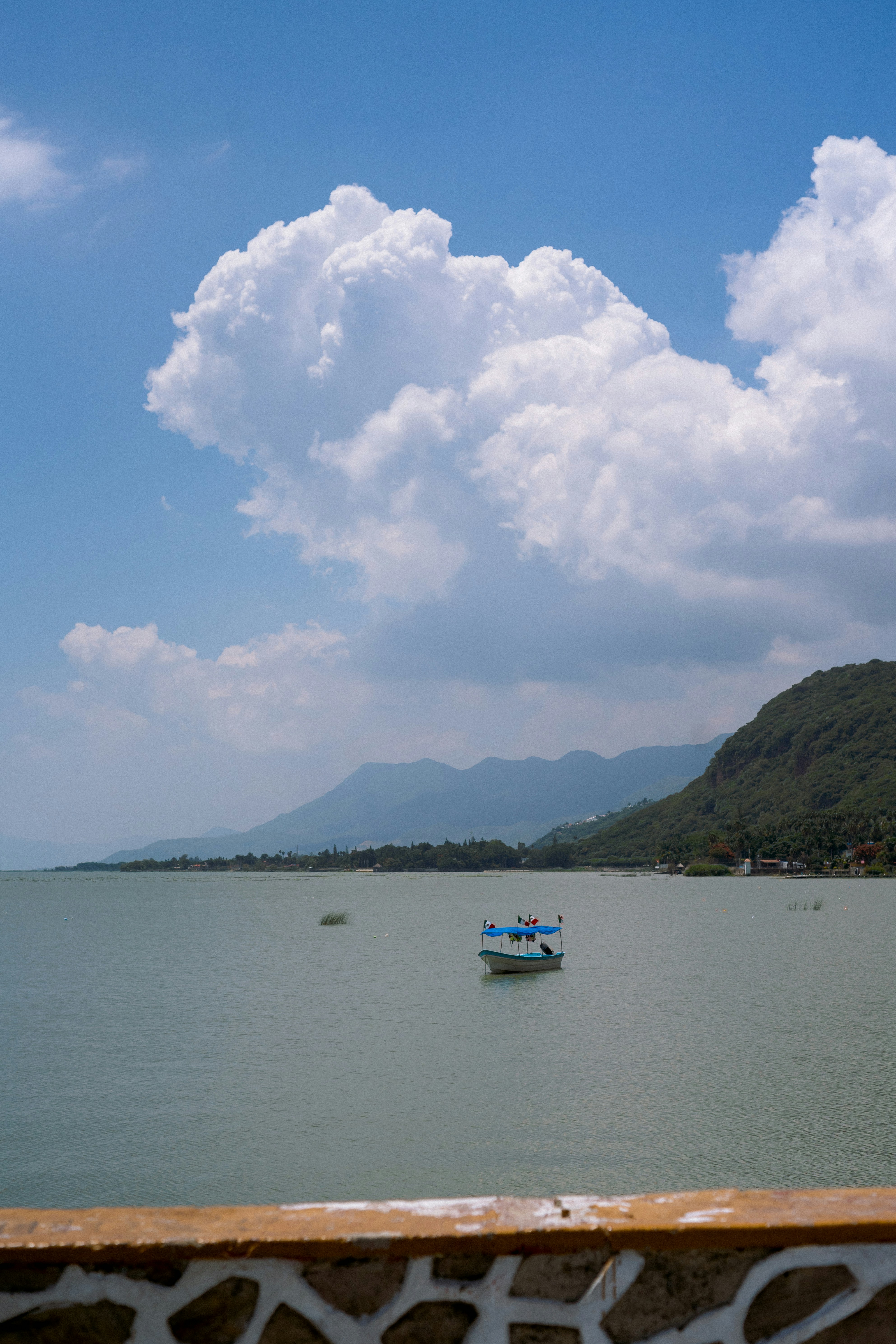 A solitary boat drifts on calm waters, framed by distant mountains and fluffy clouds, evoking a sense of peace and serenity.