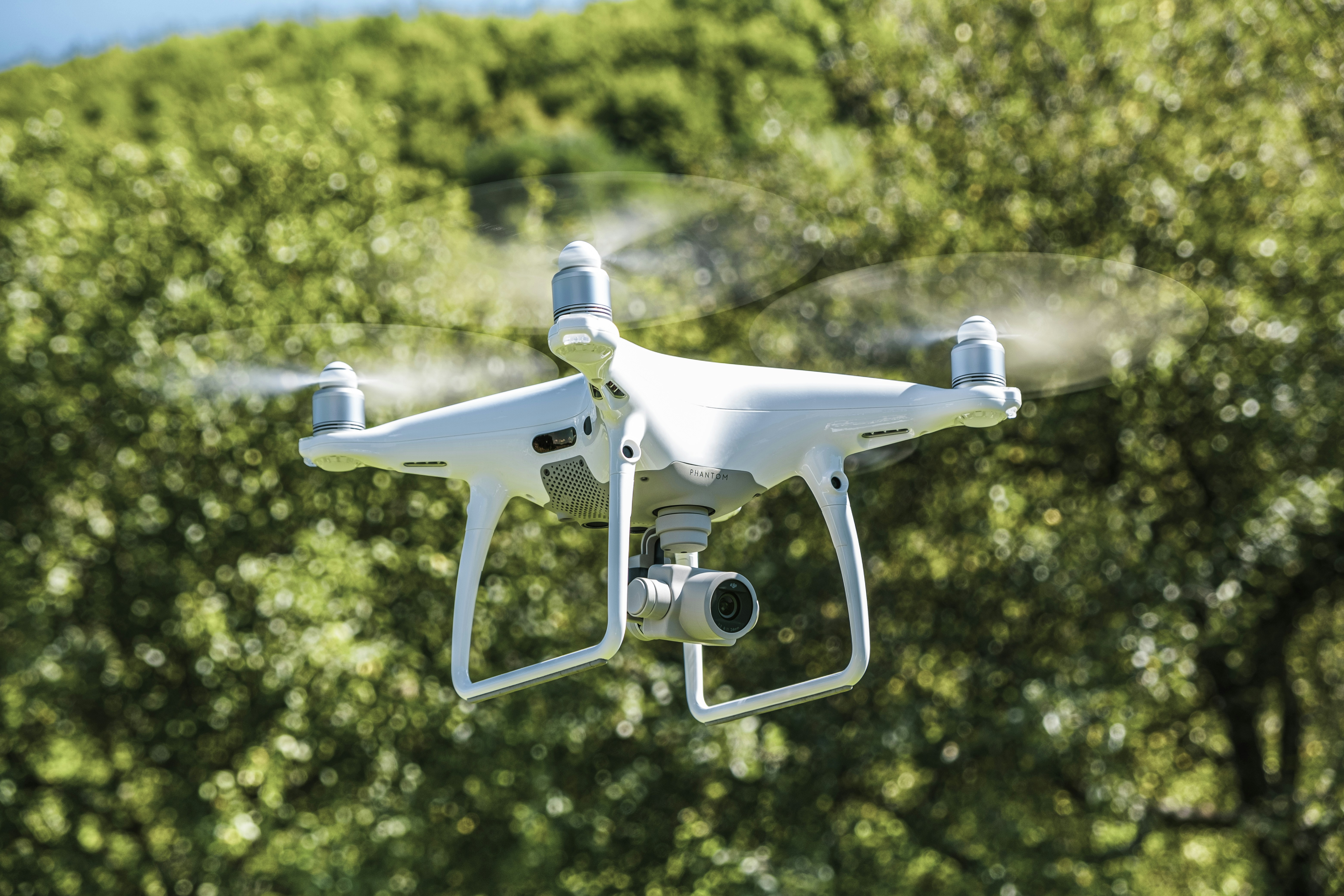Drone hovering in mid-air against a backdrop of lush greenery, showcasing advanced aerial technology.