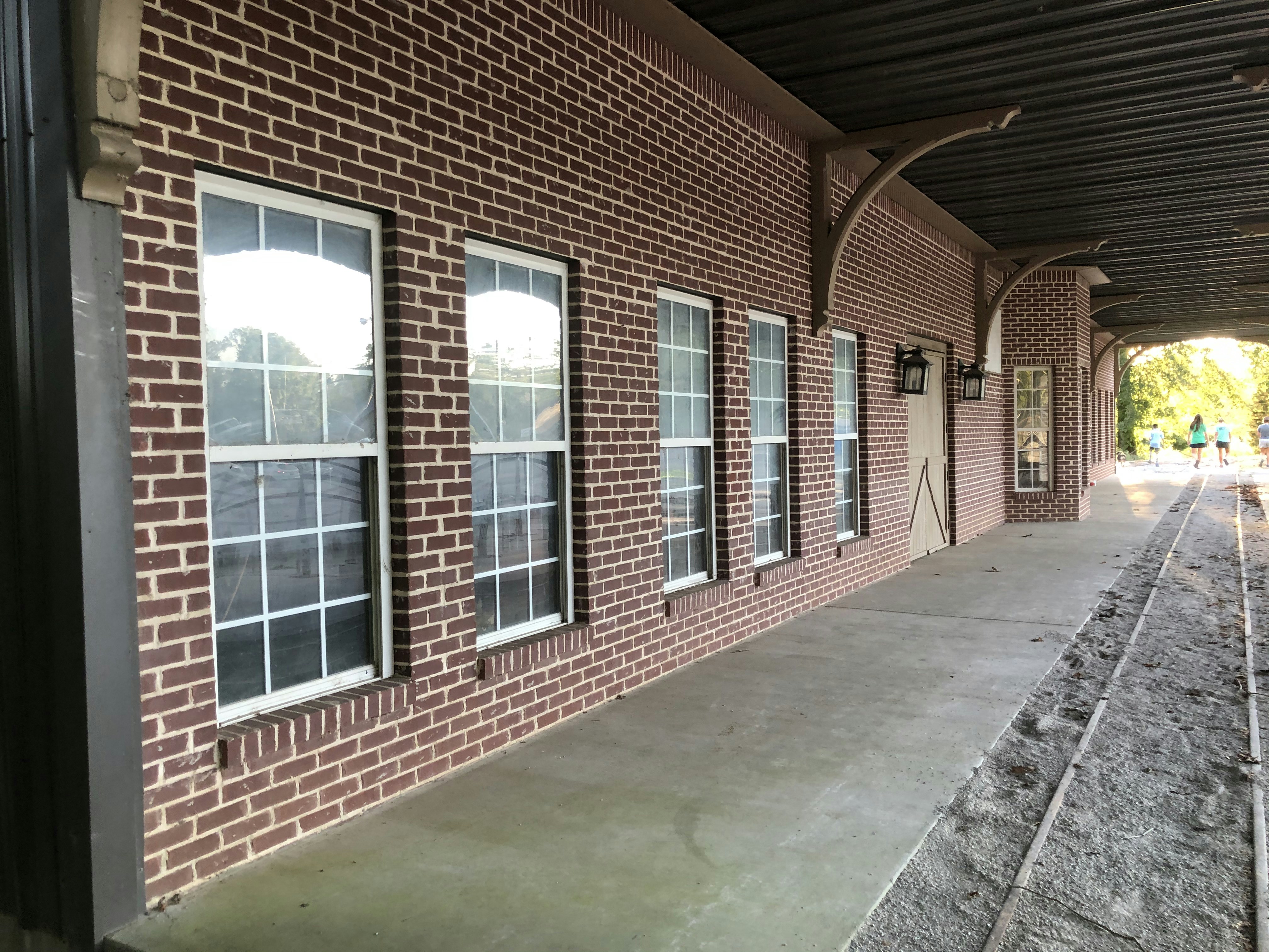 Historic train station facade featuring multiple large windows and brickwork, with a glimpse of the platform and tracks. 