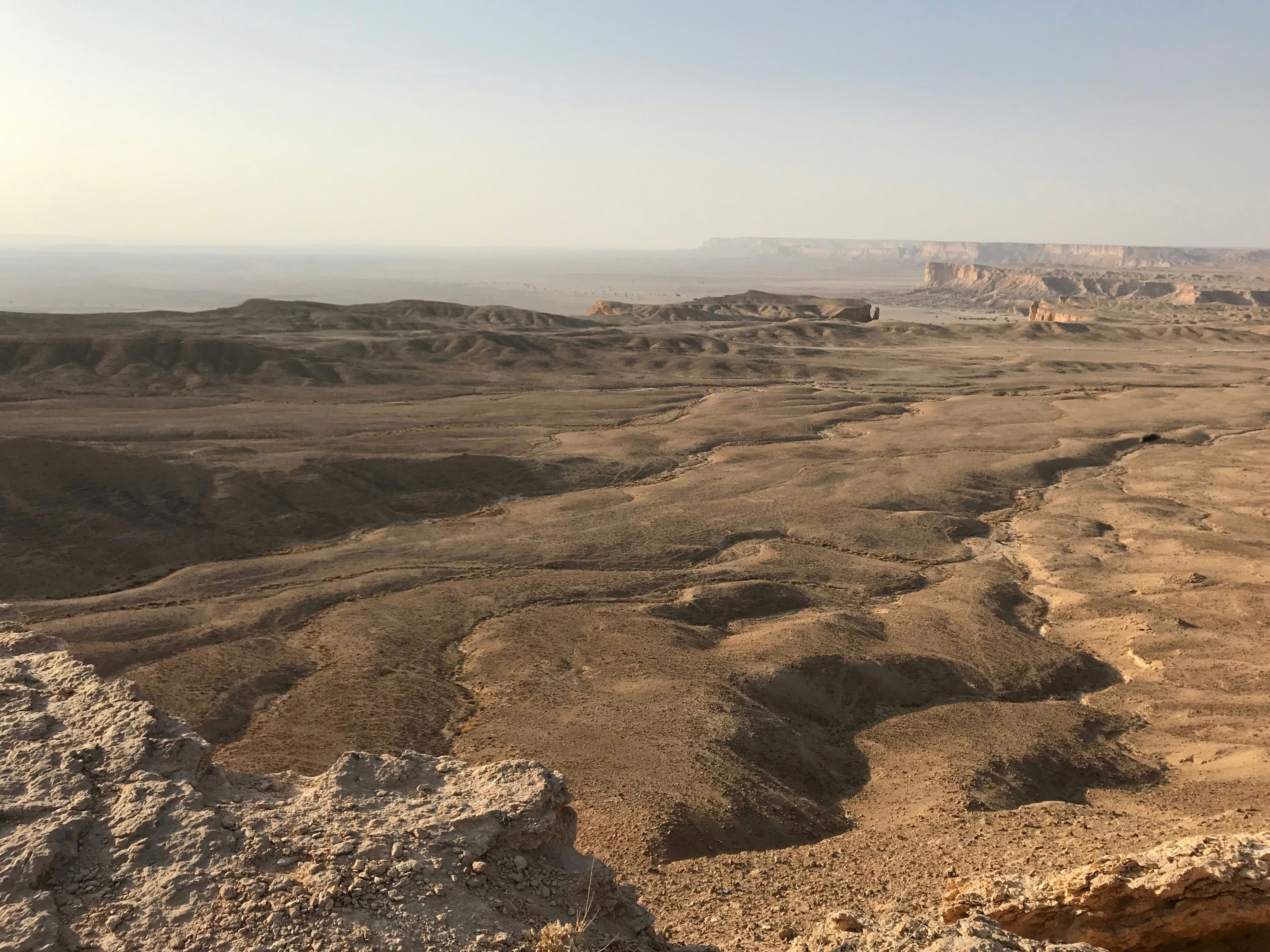 Vast desert landscape showcasing undulating terrain under a hazy sky. The rugged formations create a sense of depth and isolation.