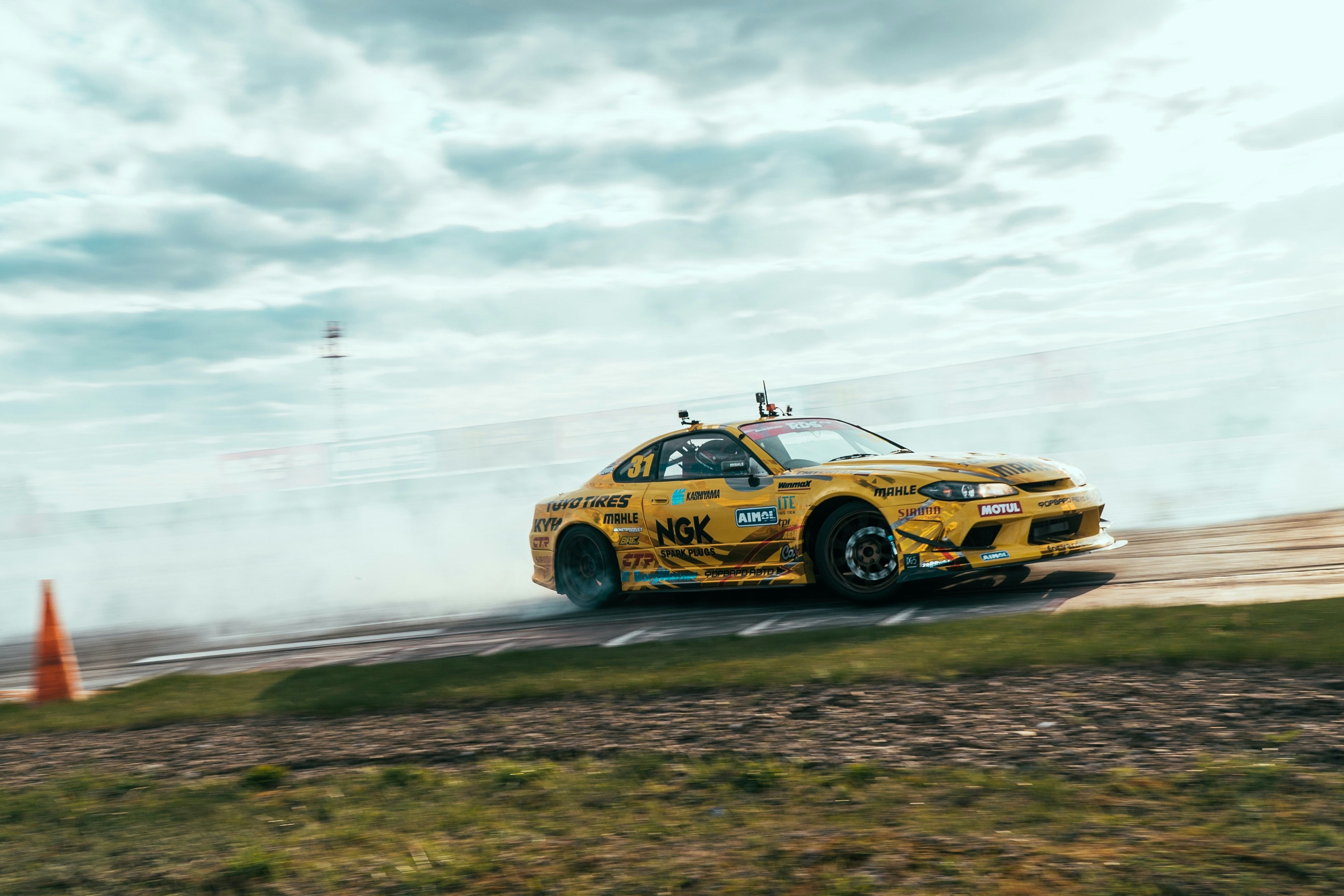 Yellow drift car maneuvering through a cloud of tire smoke on a racetrack, showcasing speed and skill.