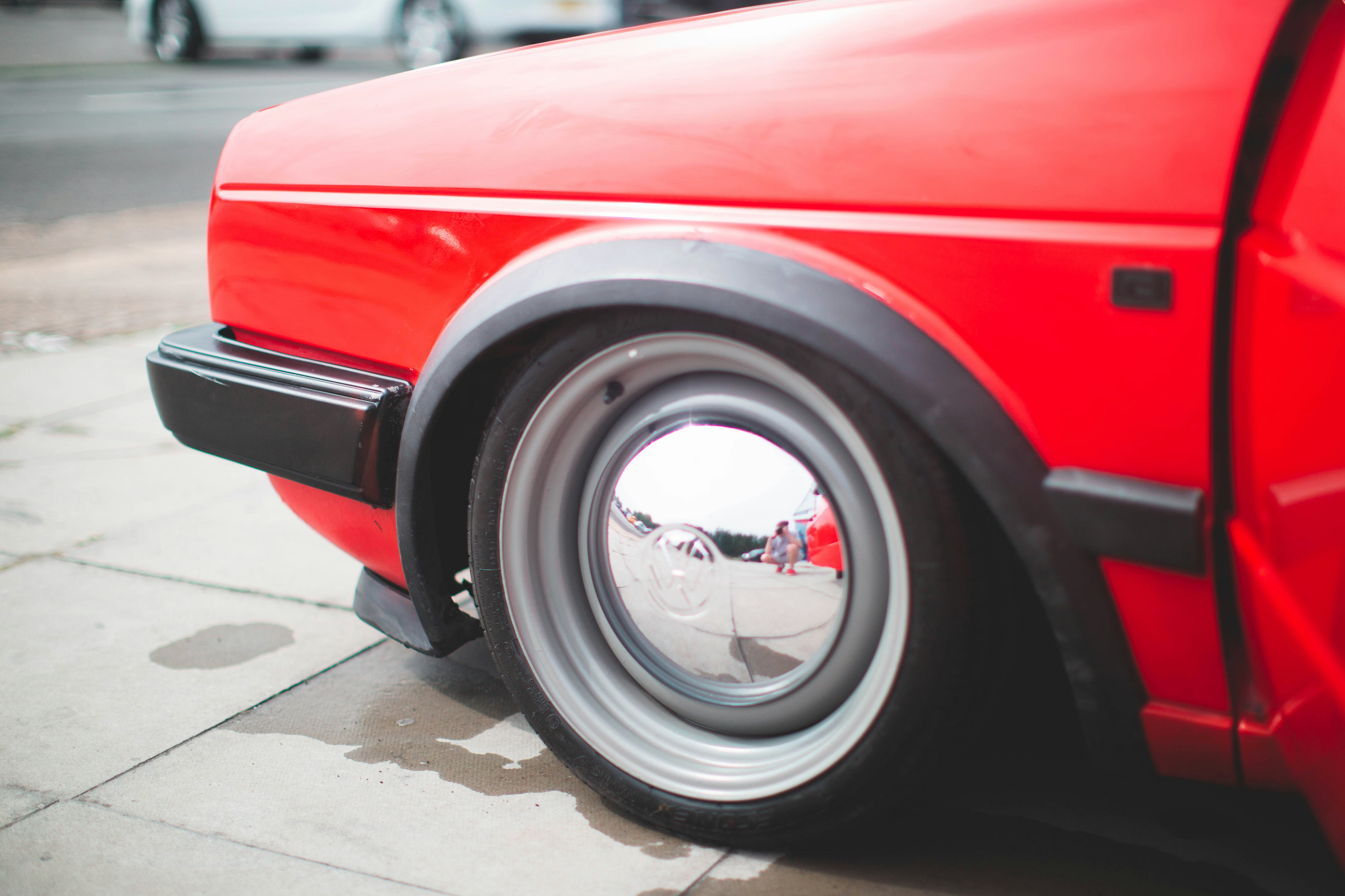 Close-up view of a red car's wheel, showcasing the polished rim and tire against a blurred urban backdrop.