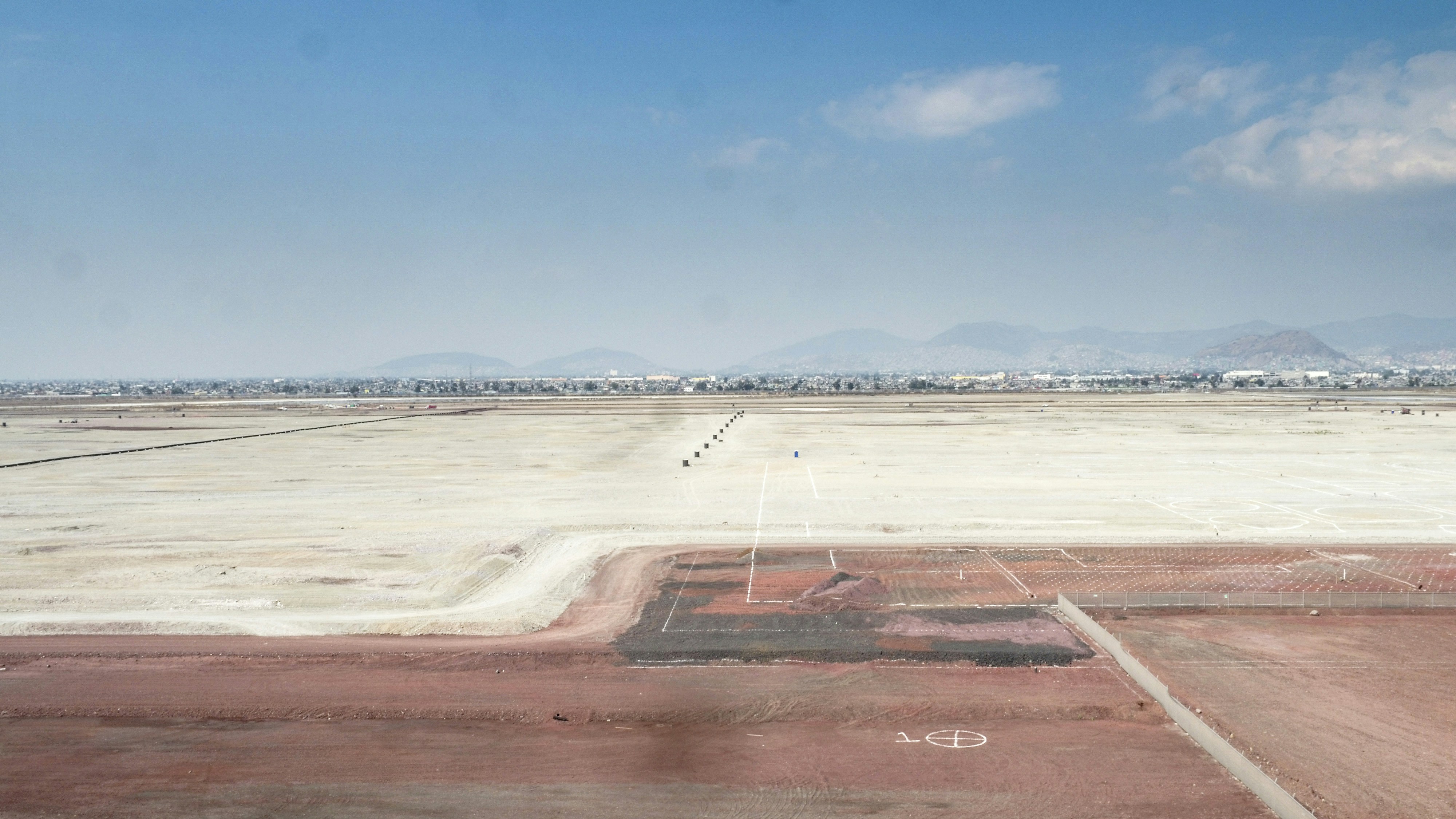 Vast salt flats stretch towards the horizon, dotted with distant vehicles and framed by a hazy skyline. The stark contrast between the earth tones and the sky creates a unique landscape.
