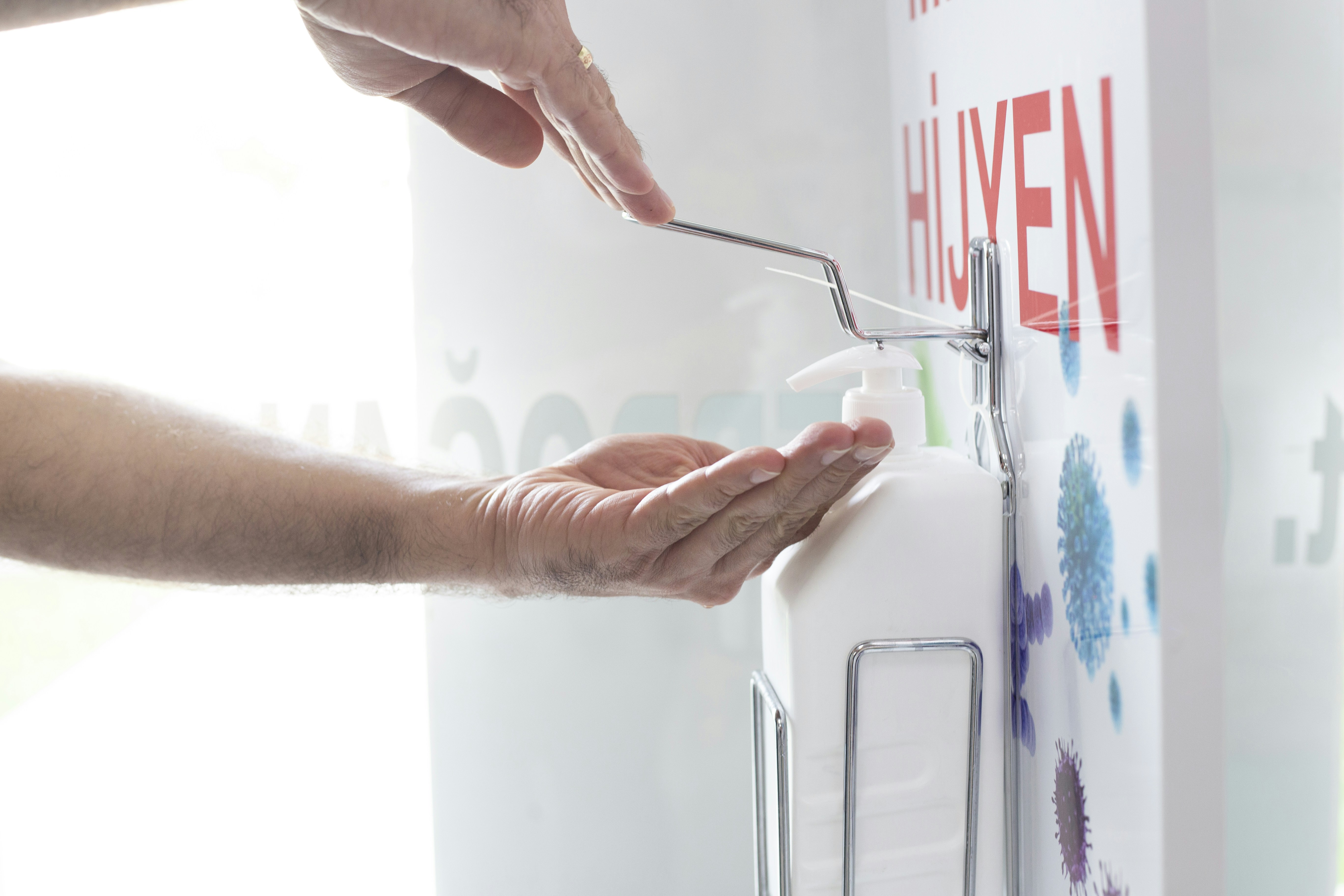Hands using a wall-mounted sanitizer dispenser.
