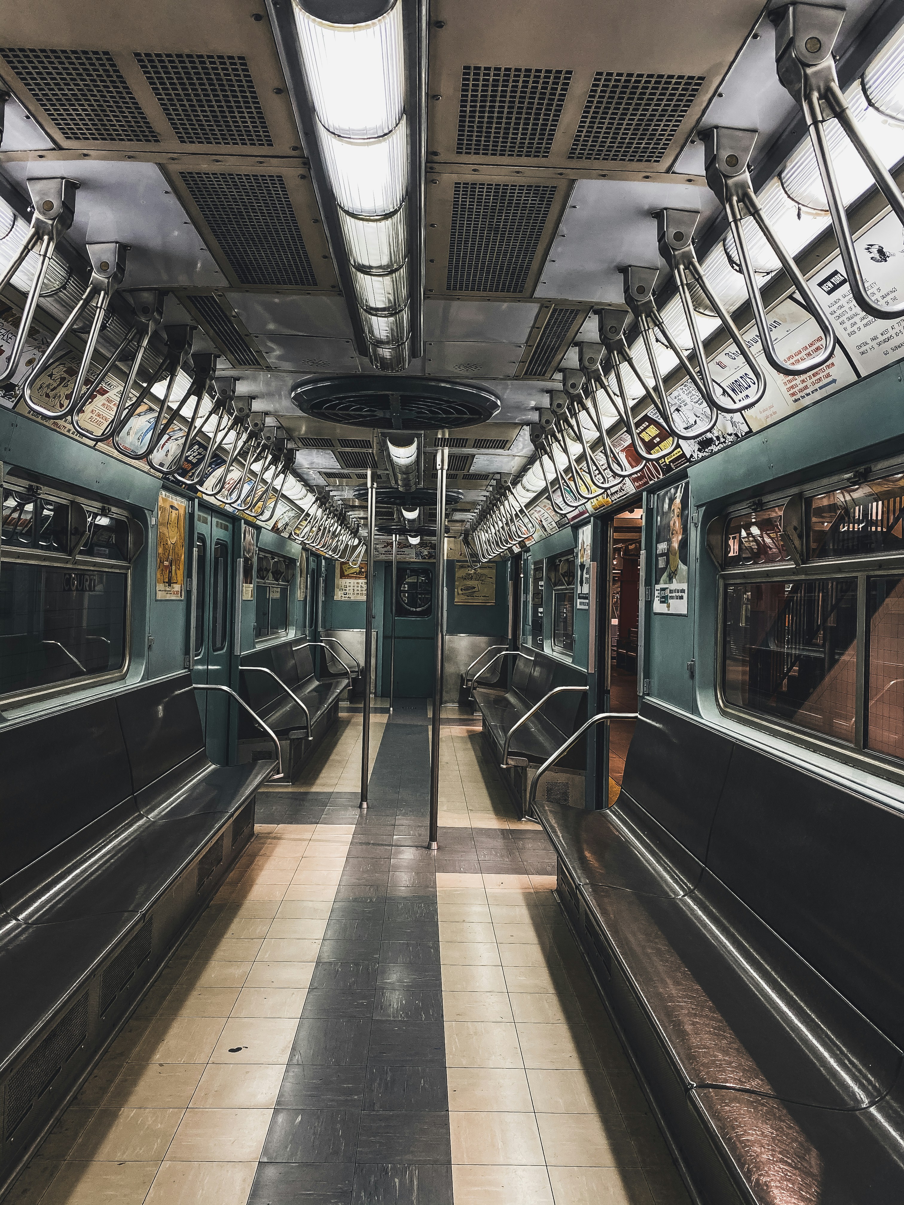 Abandoned subway car interior showcasing empty benches and overhead lighting. Vintage advertisements adorn the walls, adding character to the scene.