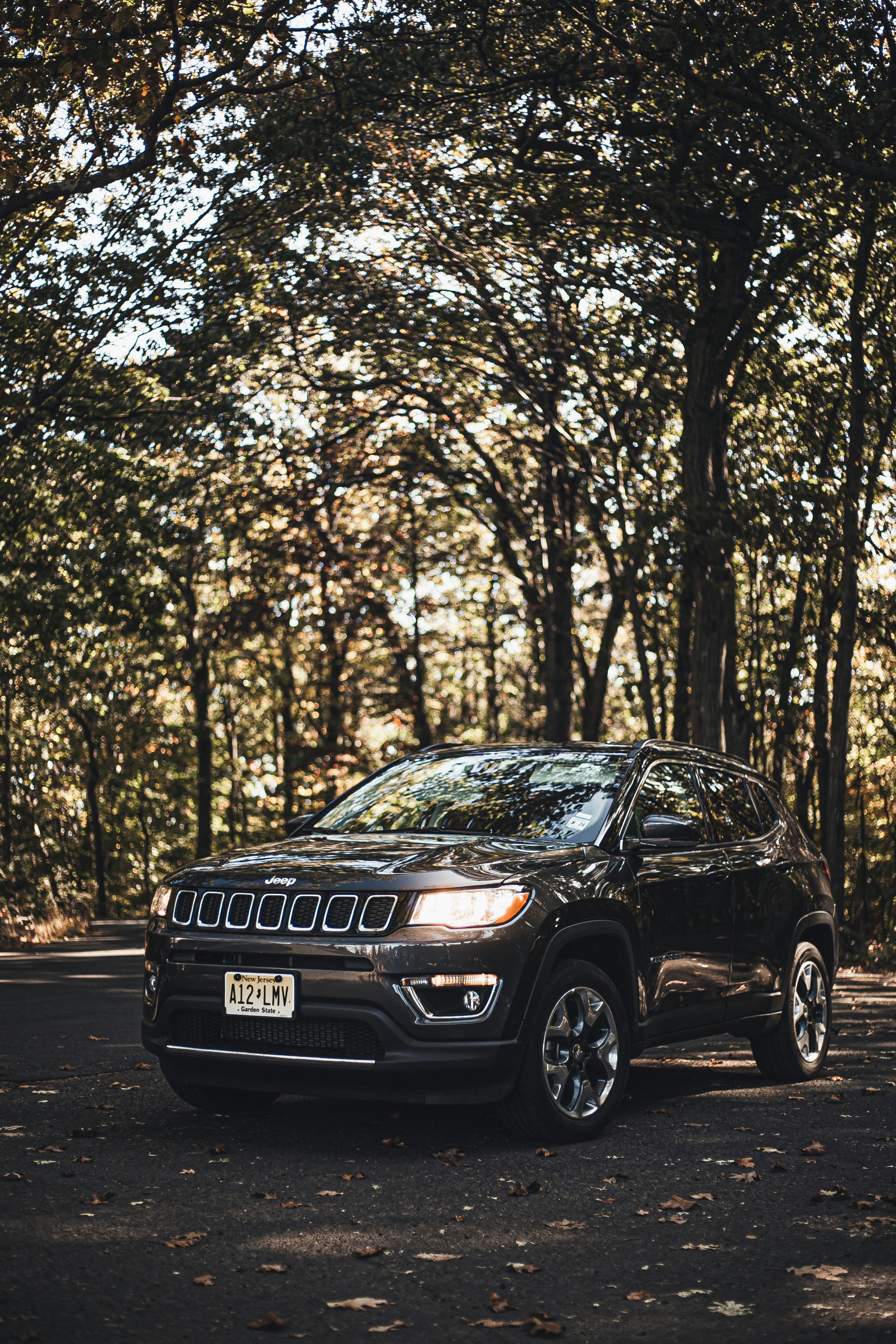 A Jeep Compass parked on a winding road surrounded by autumn foliage, showcasing its sleek design against a backdrop of vibrant trees.