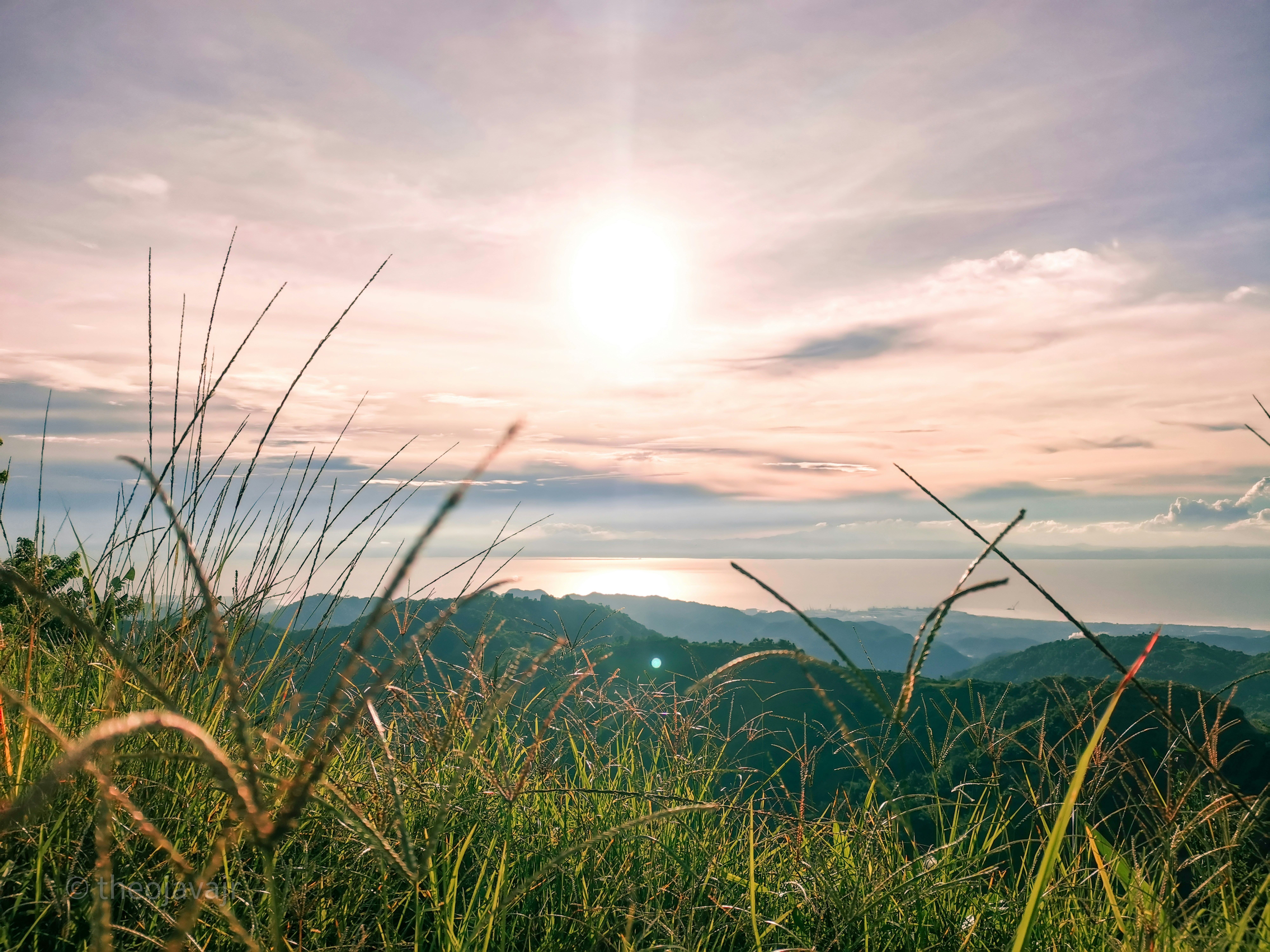 Golden sun illuminating a serene landscape of rolling hills and tall grass under a pastel sky.
