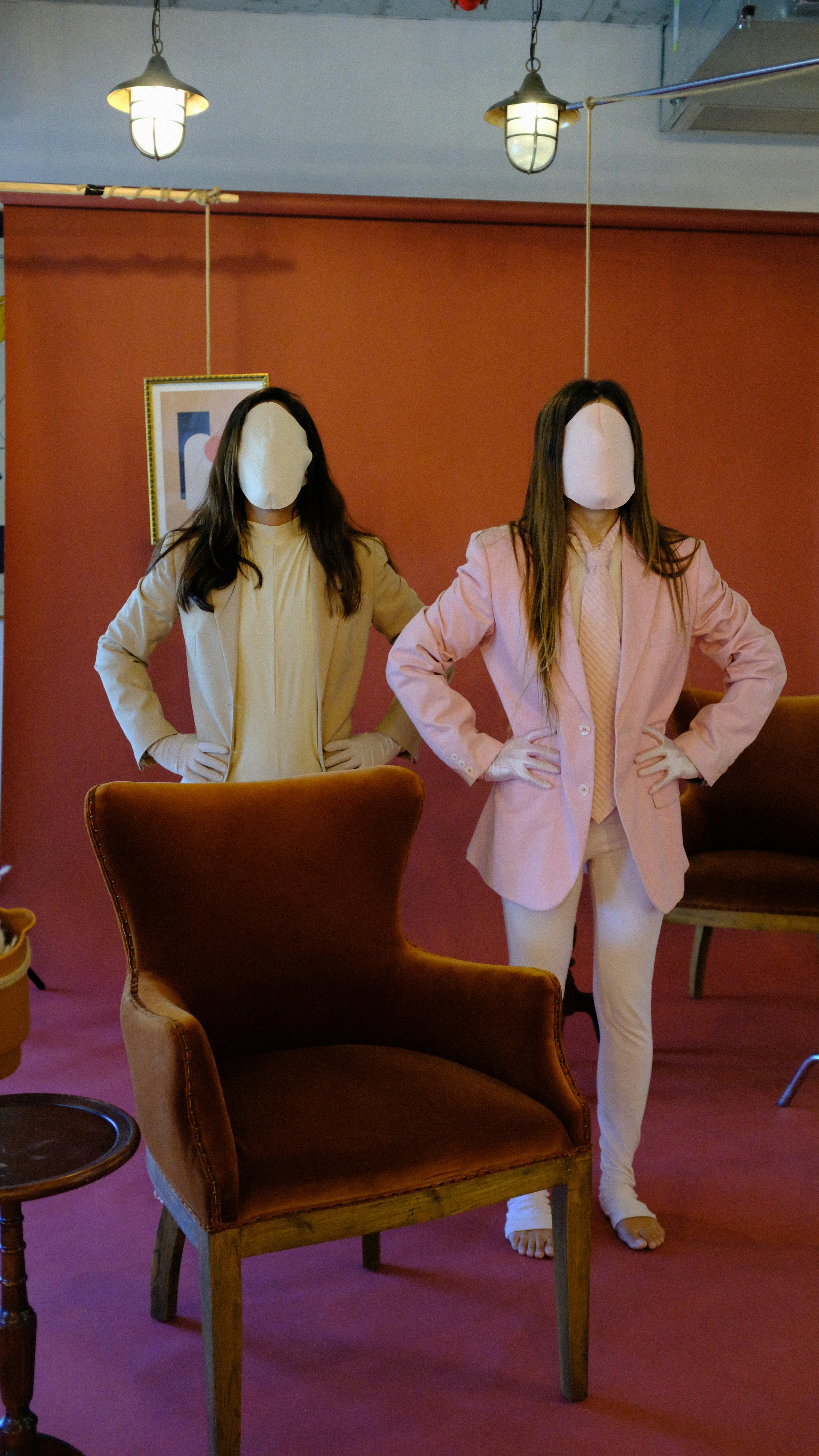 Two mannequins in tailored outfits stand confidently in a cozy setting, their faces obscured to emphasize the garments. The warm color palette creates an inviting atmosphere.