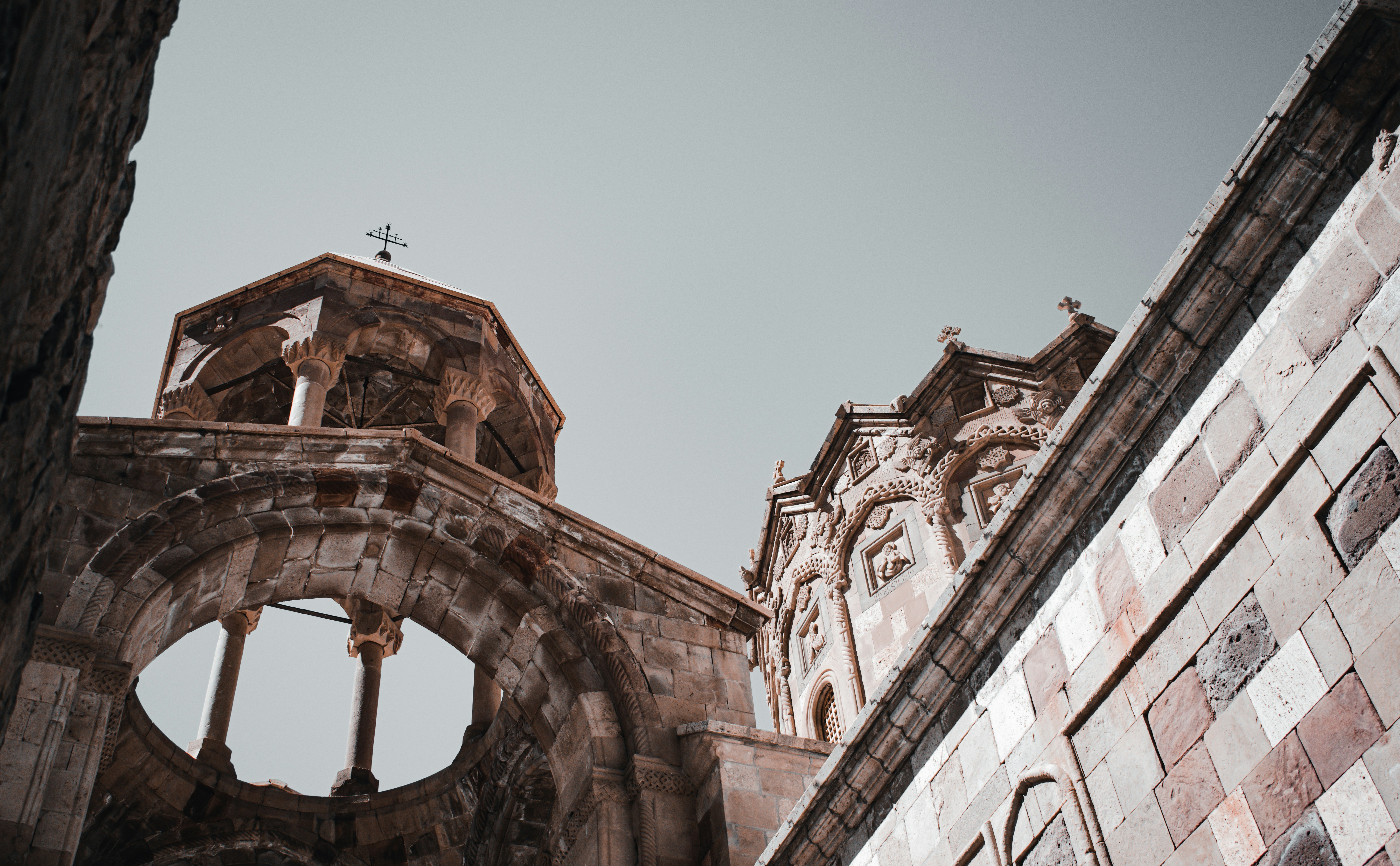 Intricate stone arches and domes of a historic church rise against a pale sky, showcasing detailed craftsmanship and a sense of grandeur.